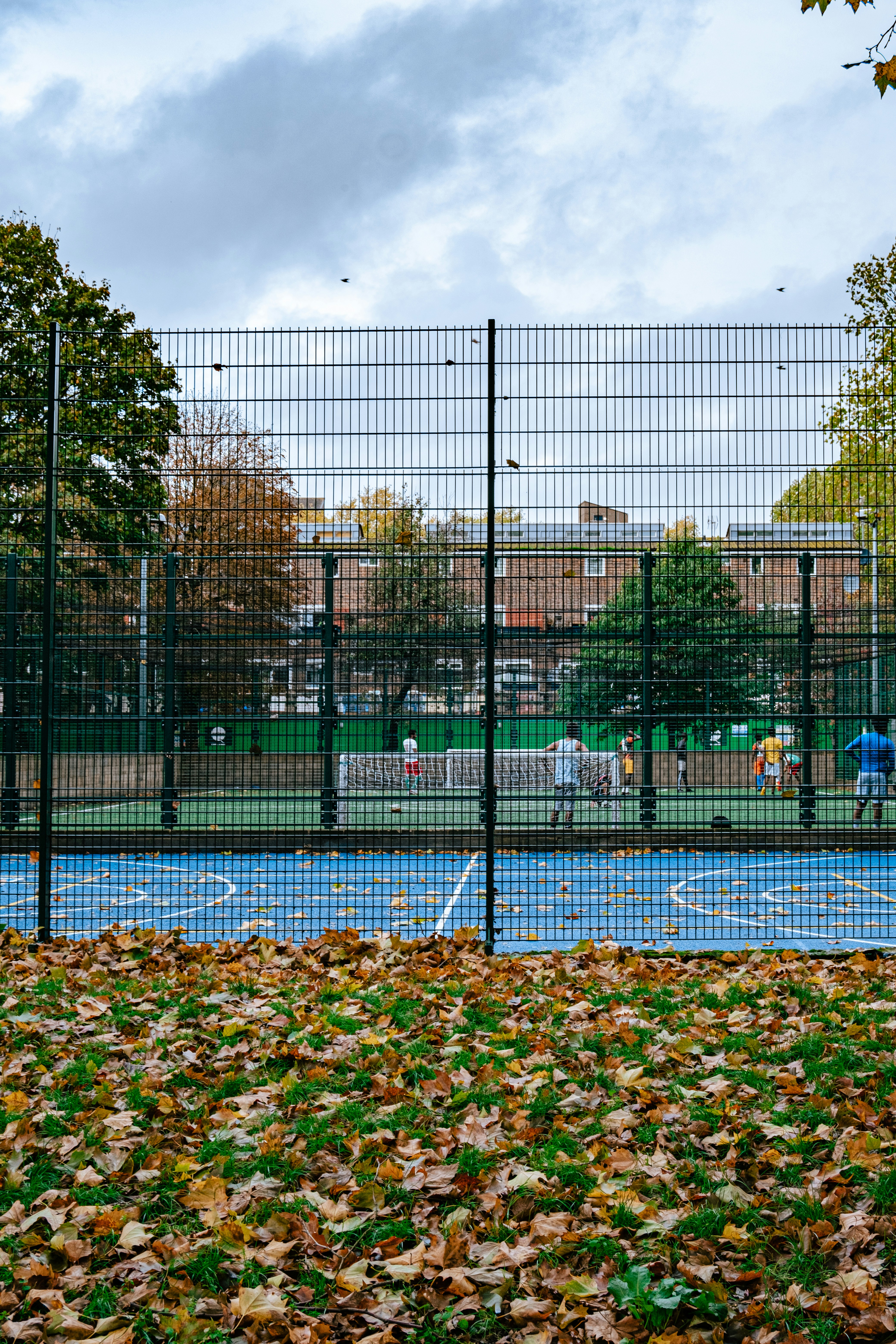 Fence-Framed Play on a Blue Court in an Autumn Park