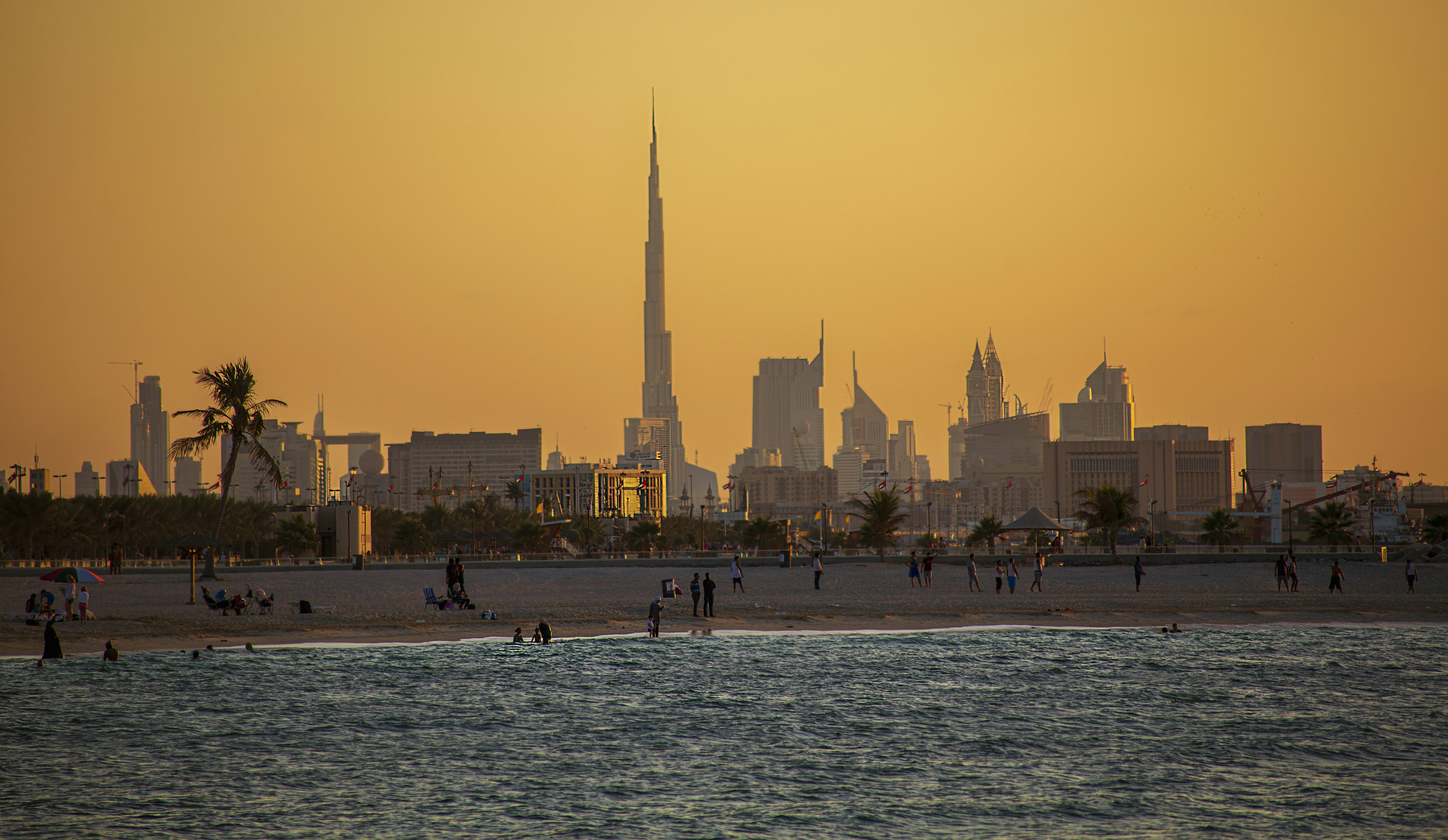 Dubai skyline silhouetted against a golden sunset, featuring iconic skyscrapers and a tranquil beach scene.