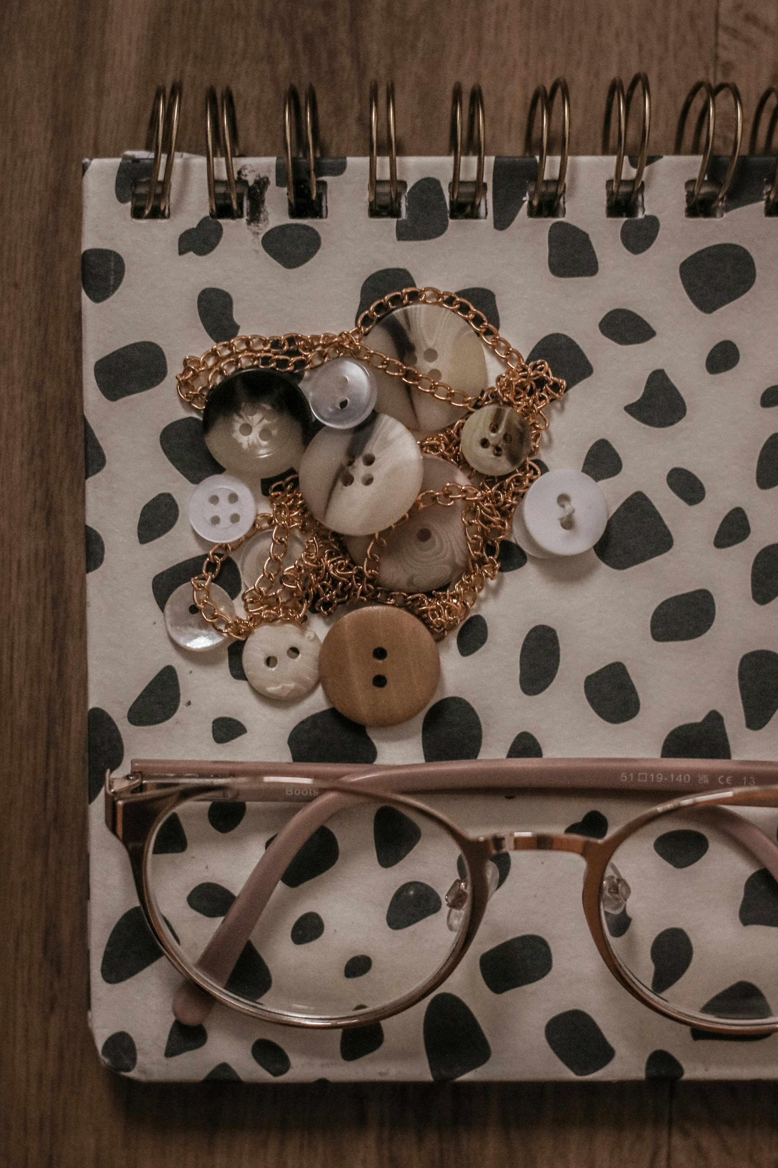 Buttoned still life: a notebook, chain jewelry, and rose-gold glasses