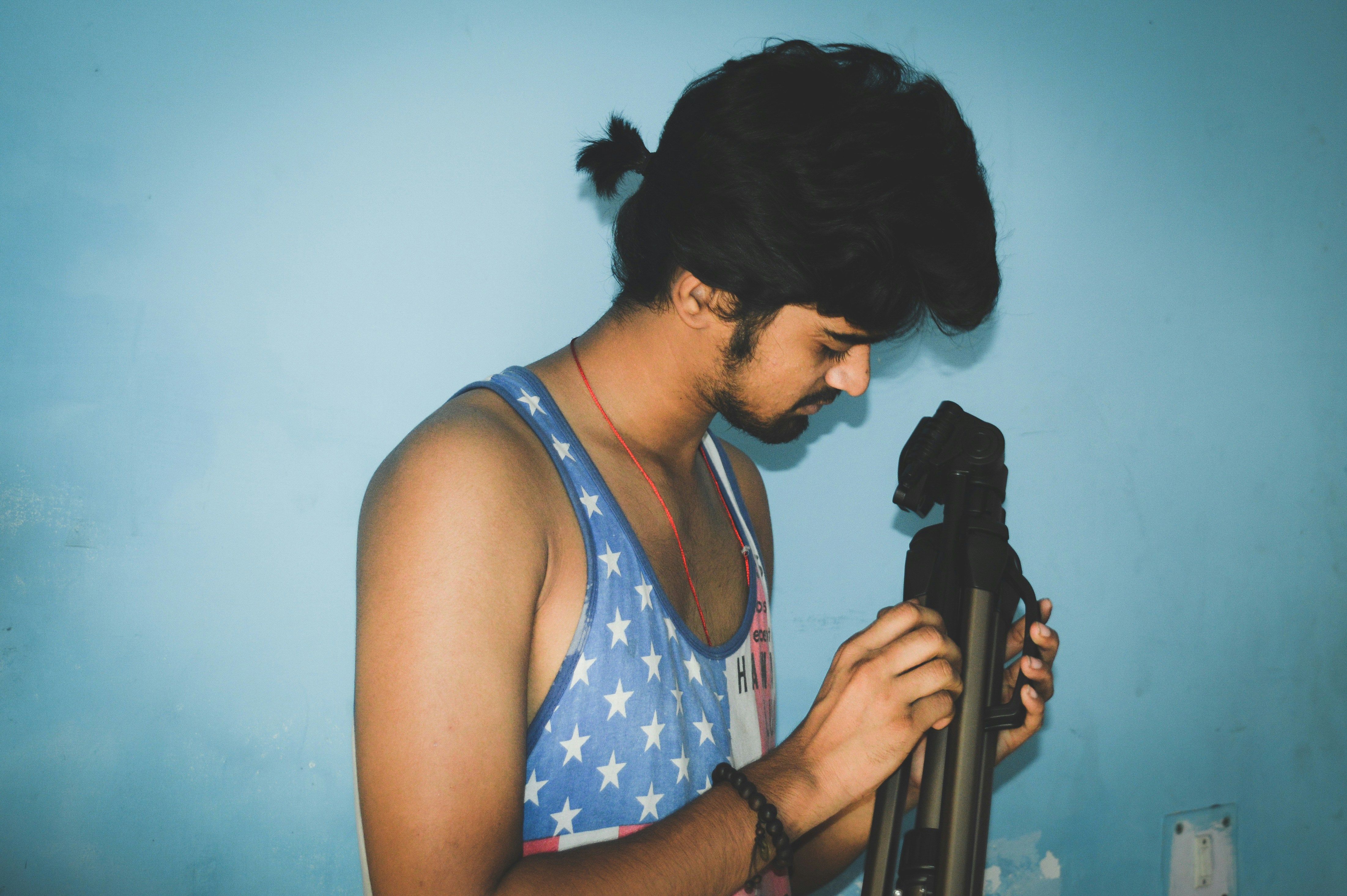 Blue Studio Moment: Hands Steady a Tripod in a Stars-and-Stripes Tank