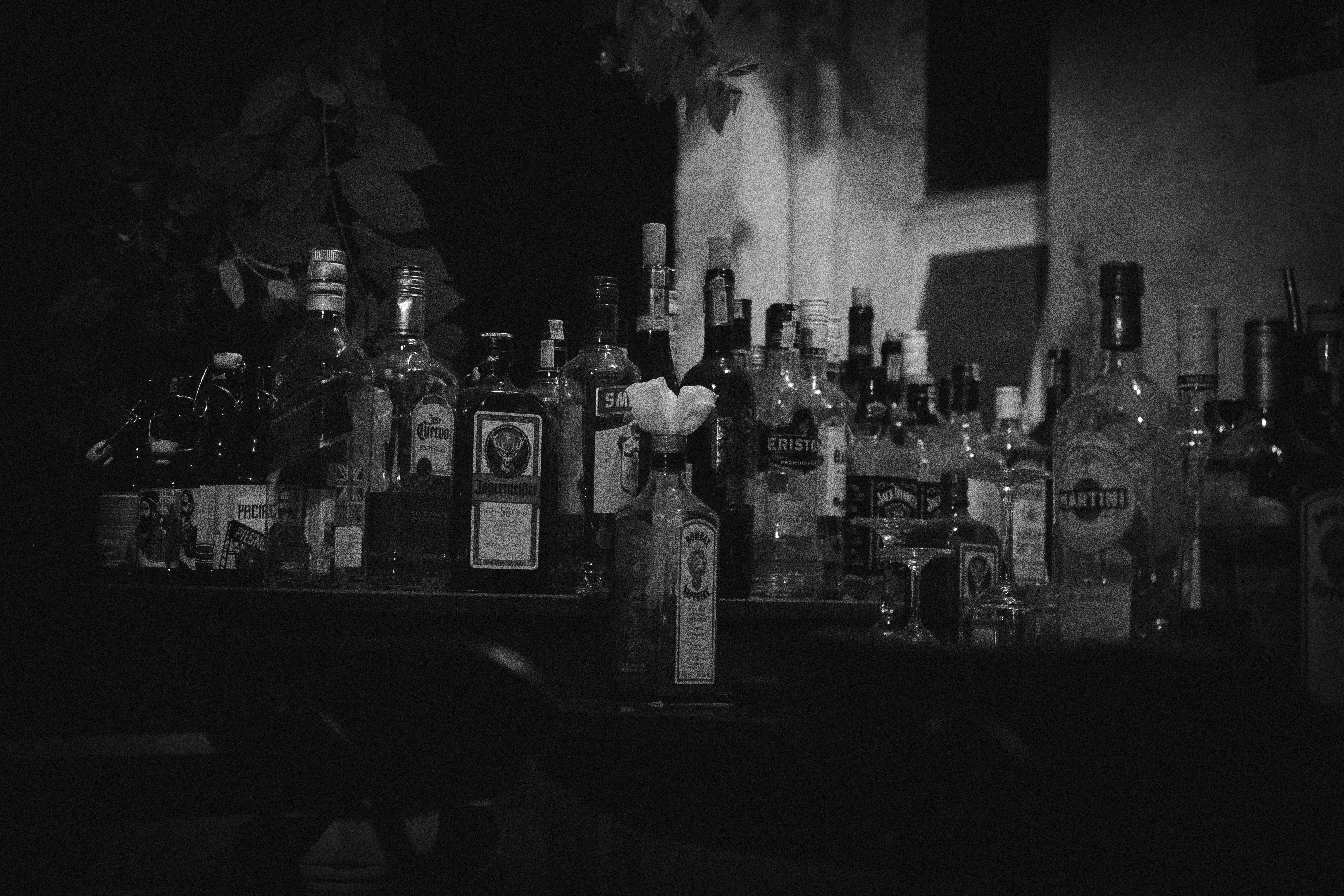 A collection of liquor bottles arranged on a table, captured in black and white, showcasing their unique shapes and labels against a dimly lit background.