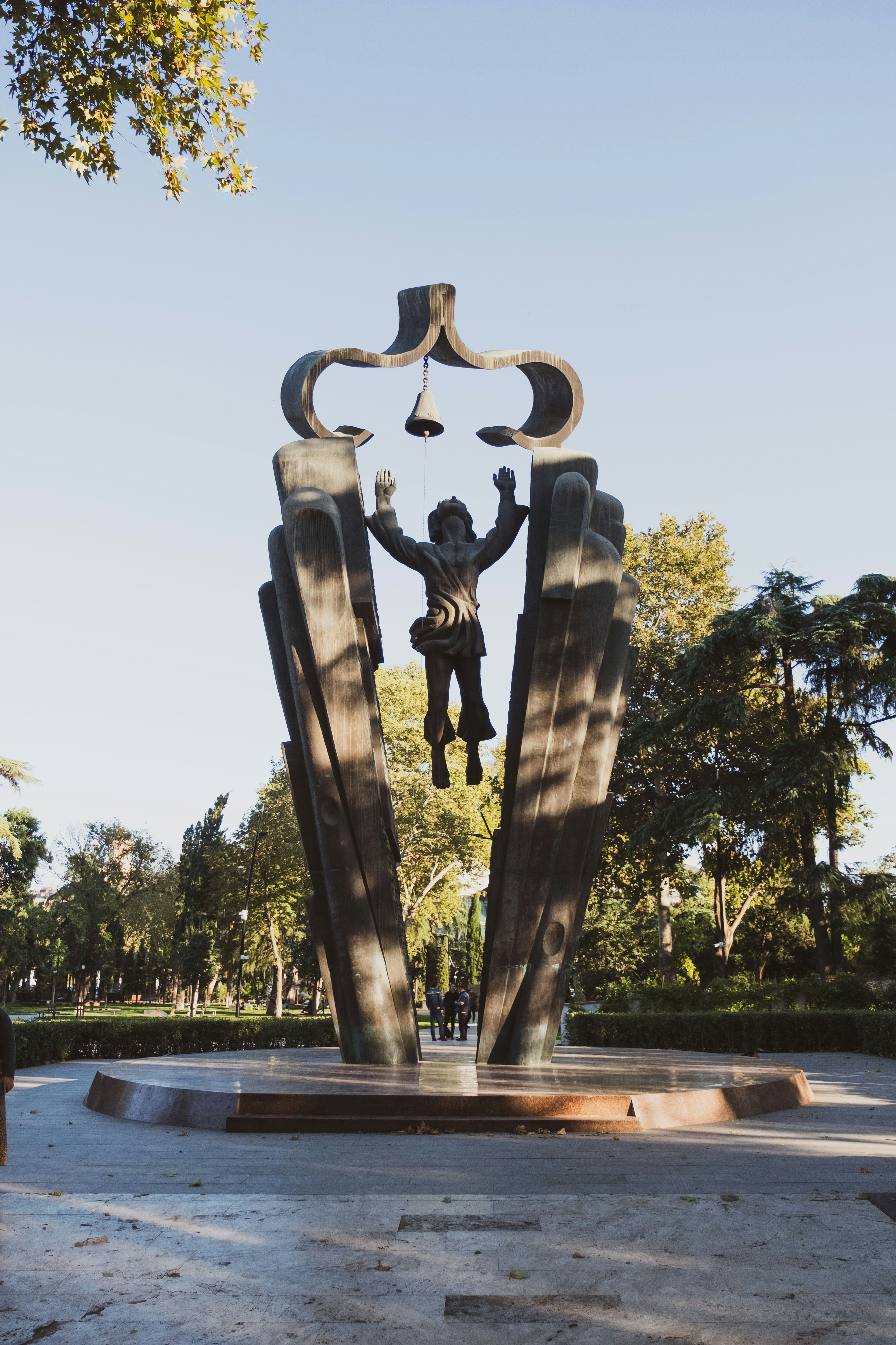 Bronze Ascension: Central Figure Between Curved Pillars Under a Clear Sky