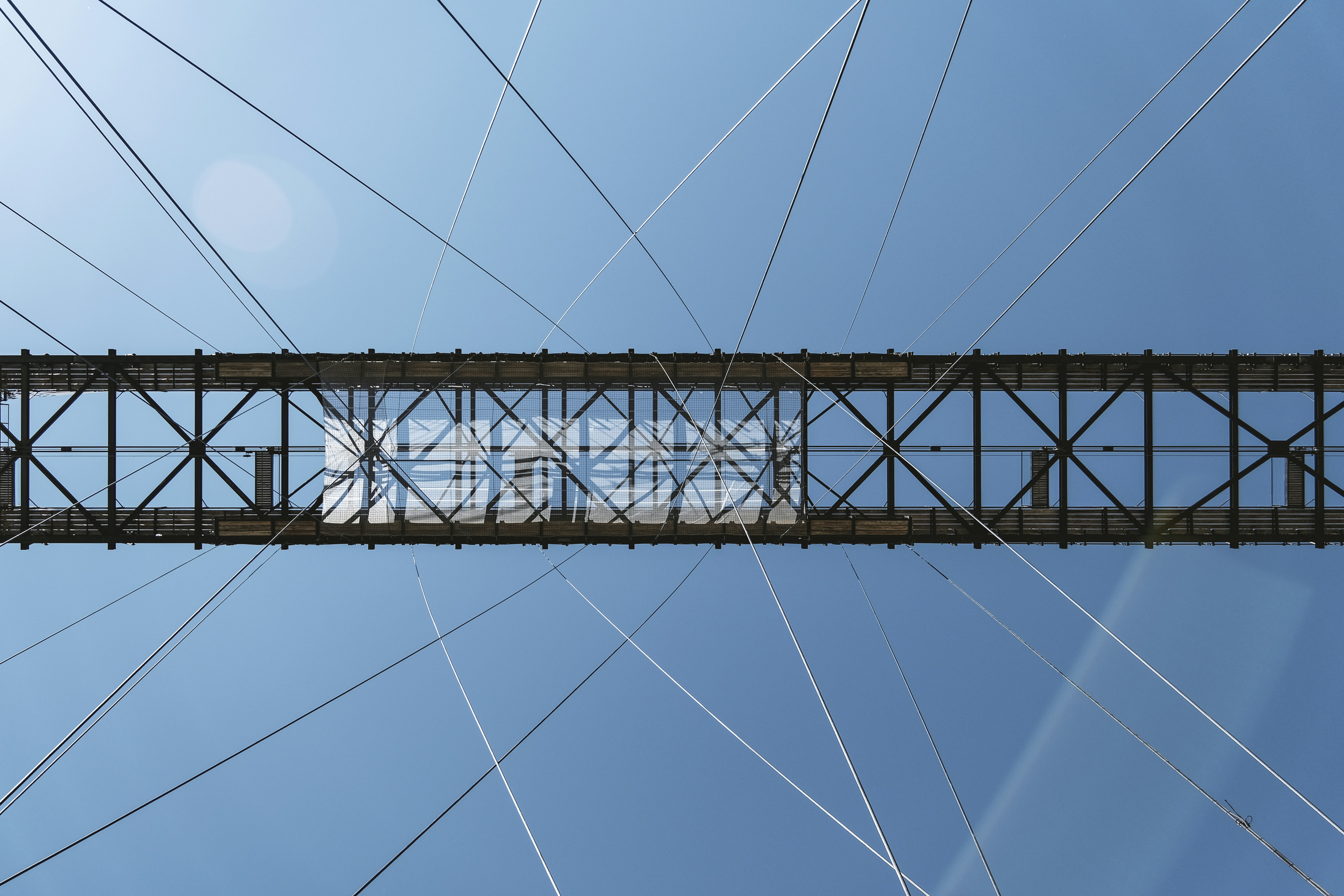 Metal structure suspended against a clear blue sky with intersecting cables.