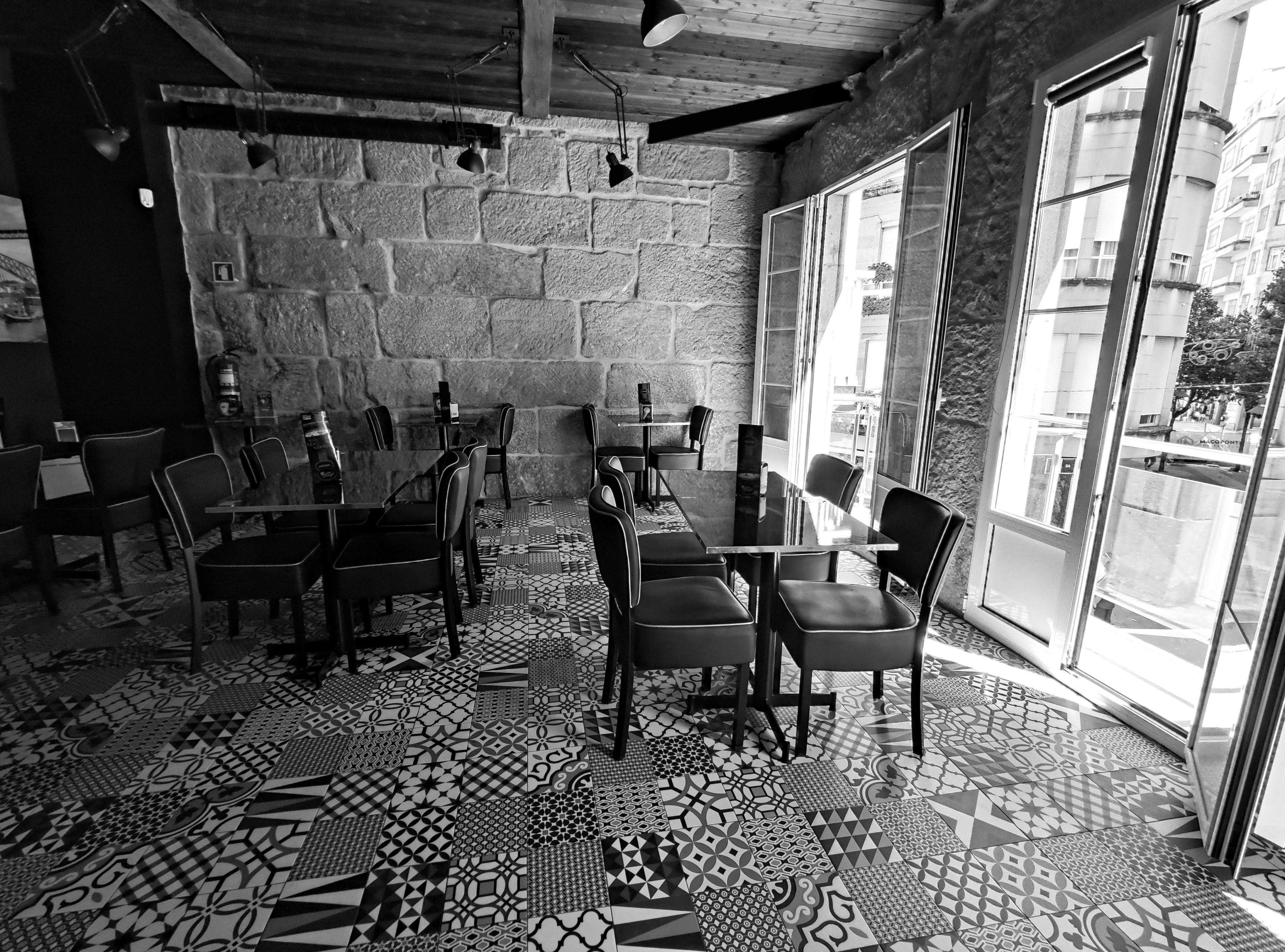 Black and white interior of a café with patterned floor tiles and sunlight streaming through open doors.