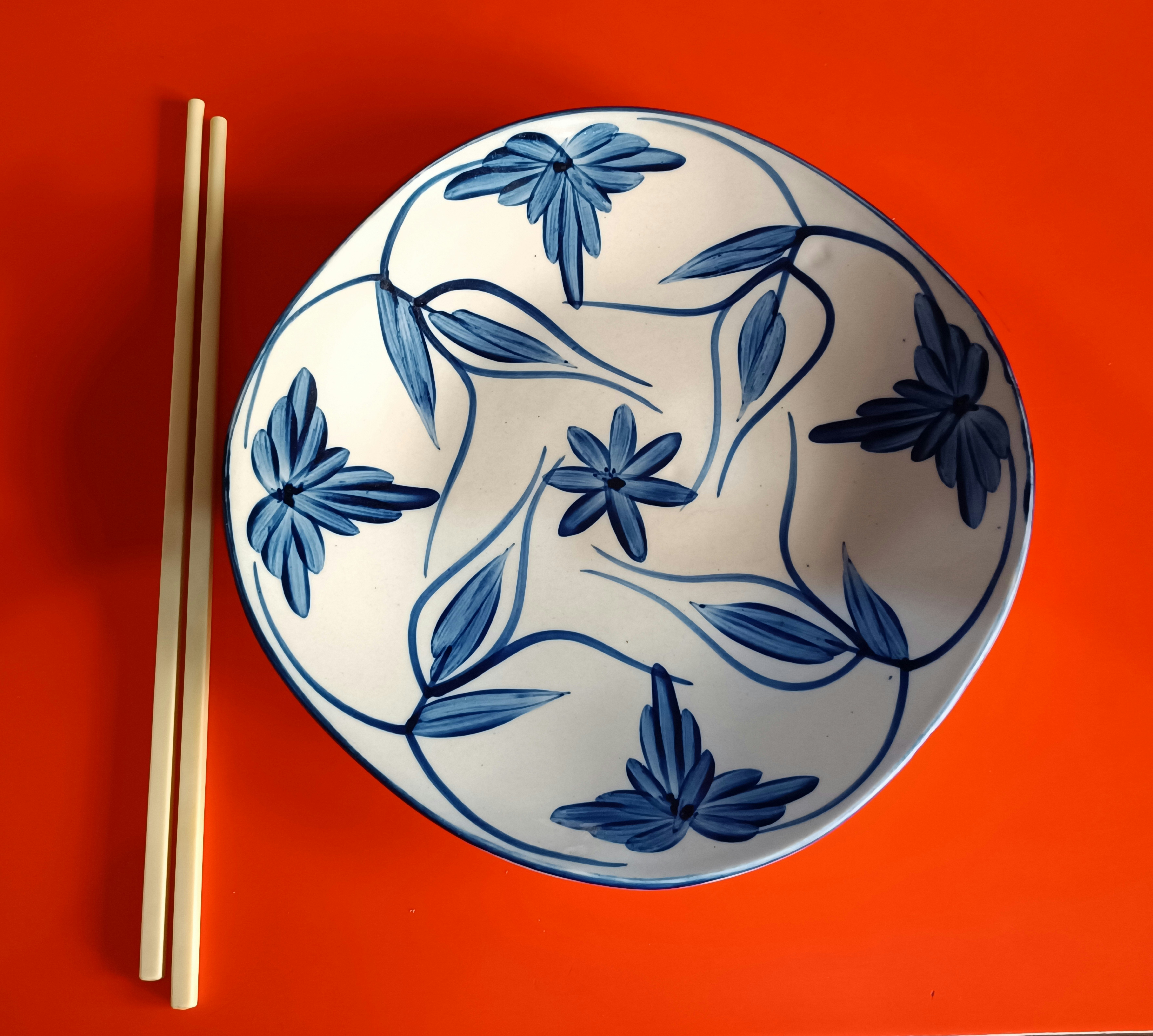 Blue-and-white ceramic plate with floral motifs sits on a vivid orange background. A pair of chopsticks lies to the left, completing this still-life setup.