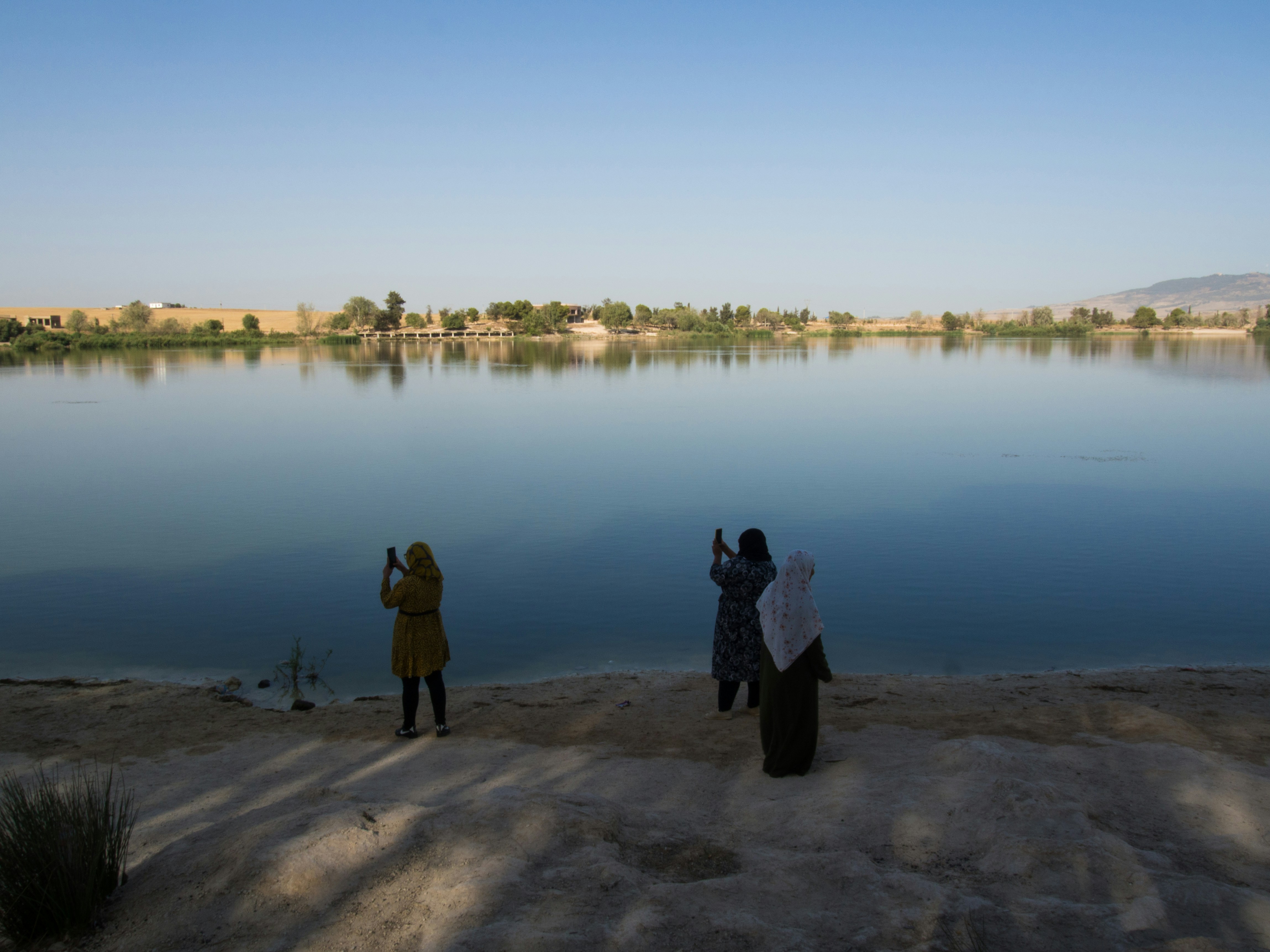 A group of people standing on a beach looking at a body of water photo ...