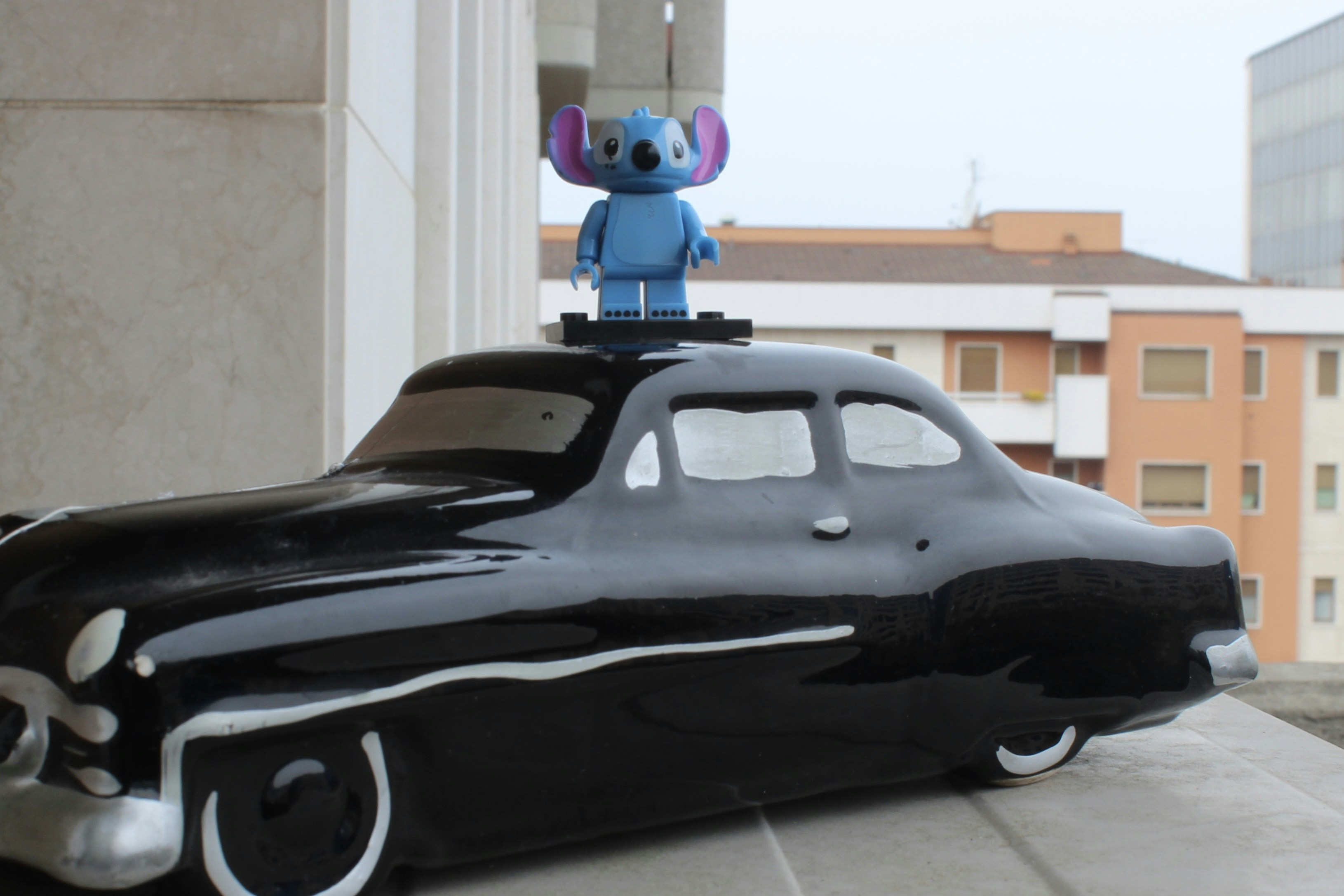Toy Koala on a glossy vintage car sculpture under urban backdrop