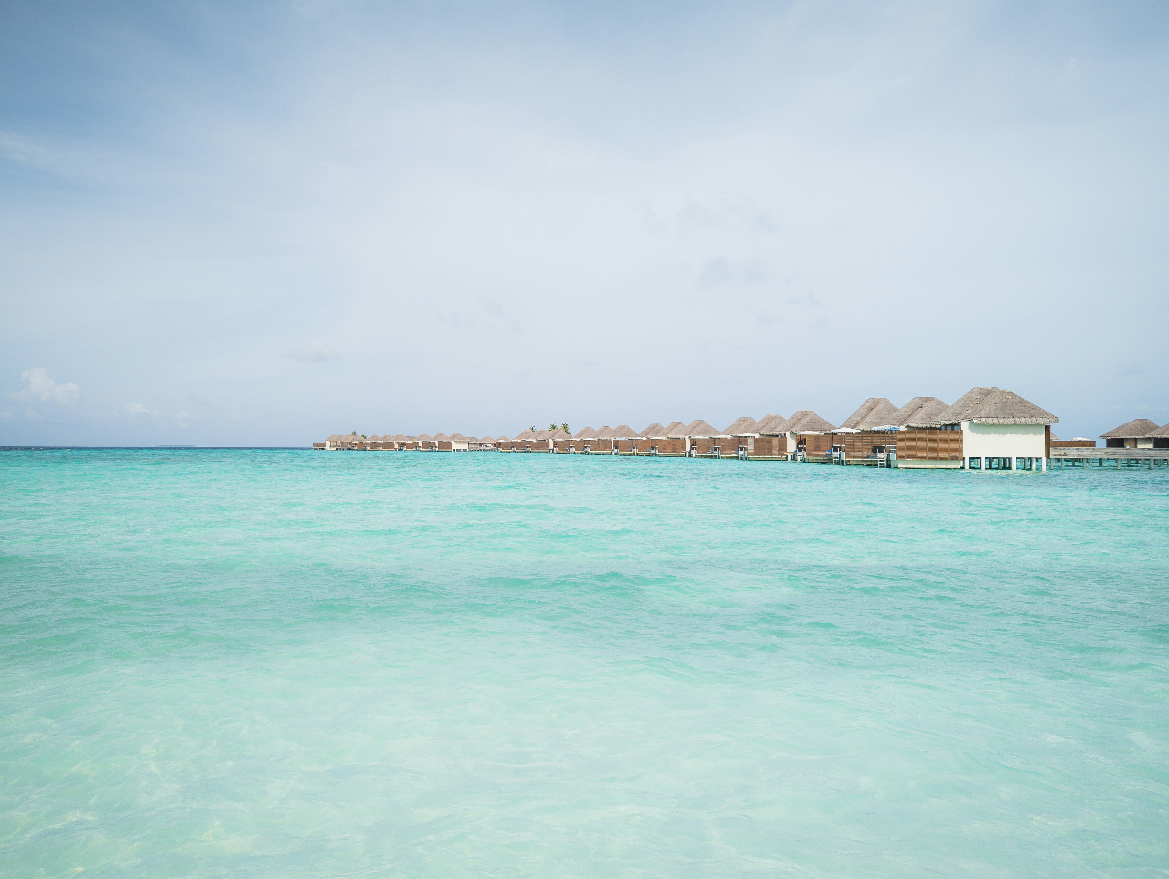Overwater bungalows line the horizon against a tranquil turquoise sea, creating a serene coastal atmosphere.