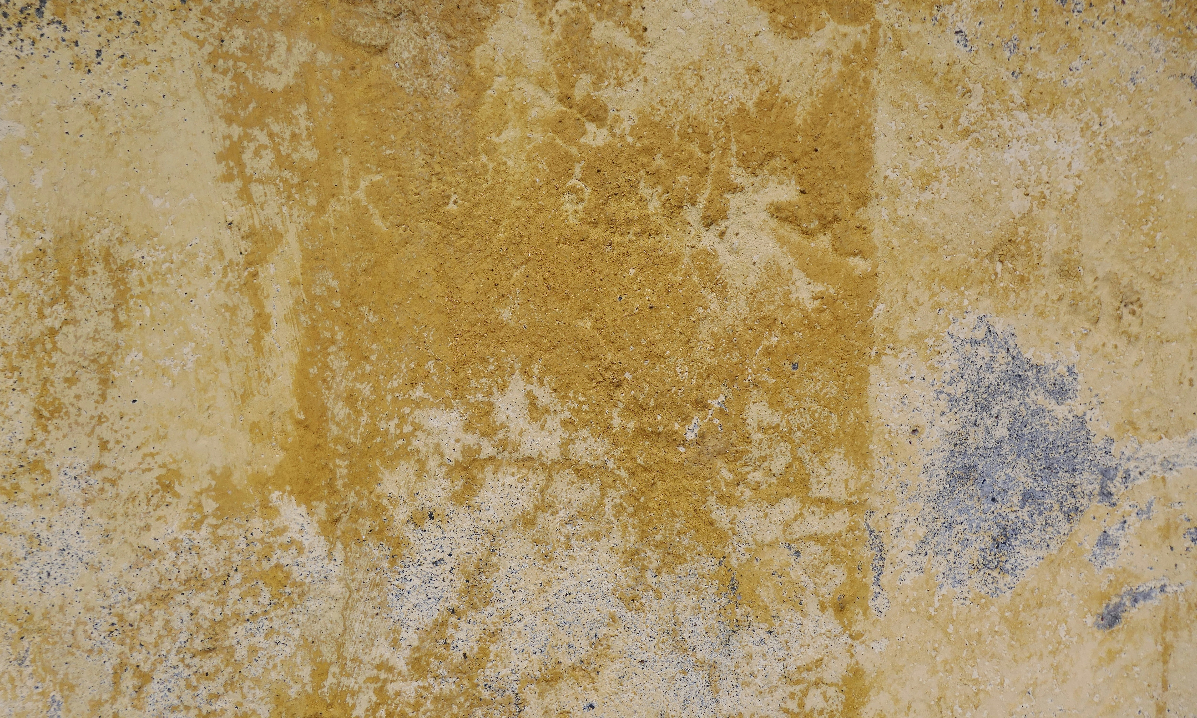 Abstract surface featuring a blend of yellow and blue hues, showcasing the natural wear and tear of a wall. The unique patterns evoke a sense of history.