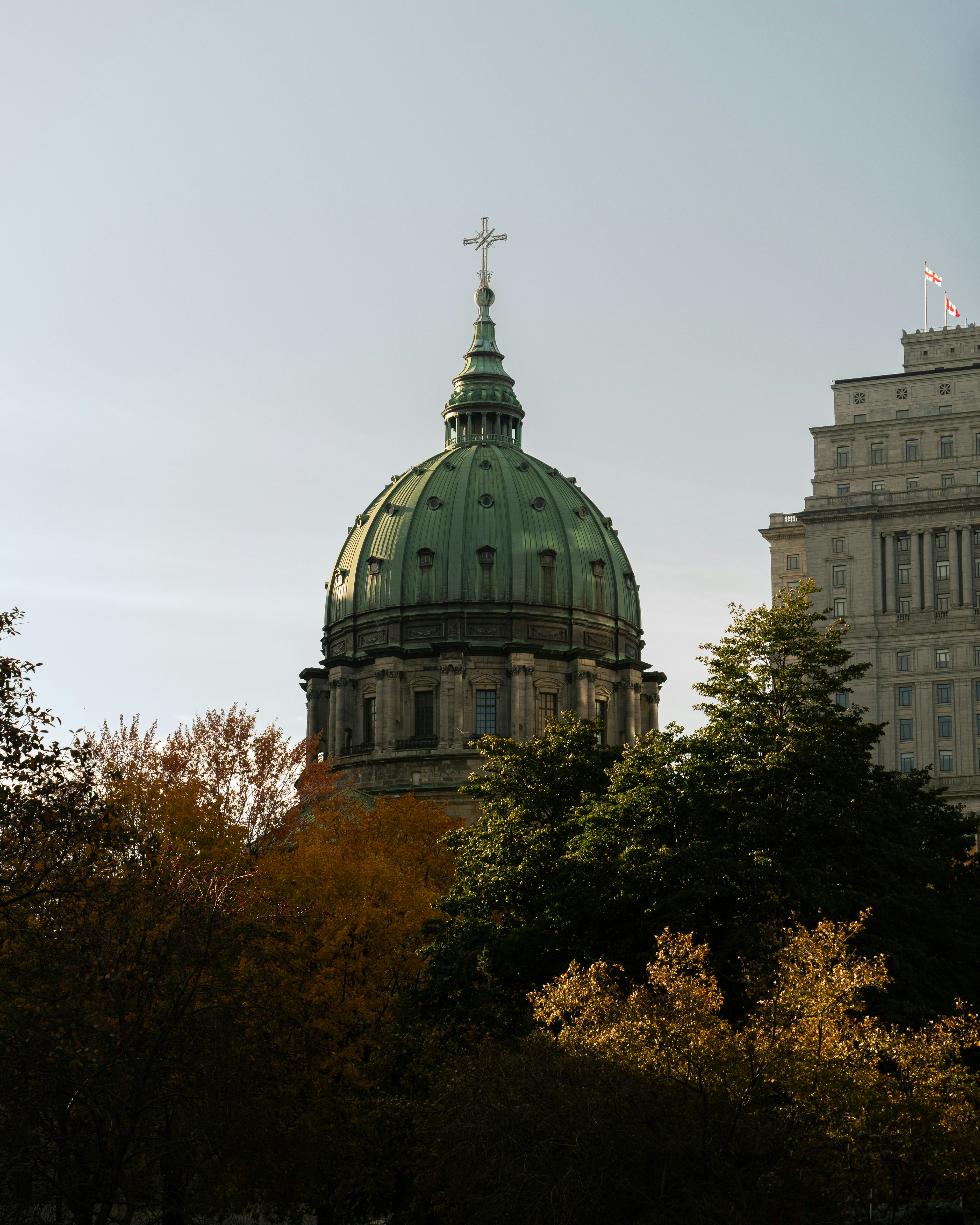 Green-domed building peeking through autumn foliage with a backdrop of a historic structure. A blend of natural and architectural beauty.