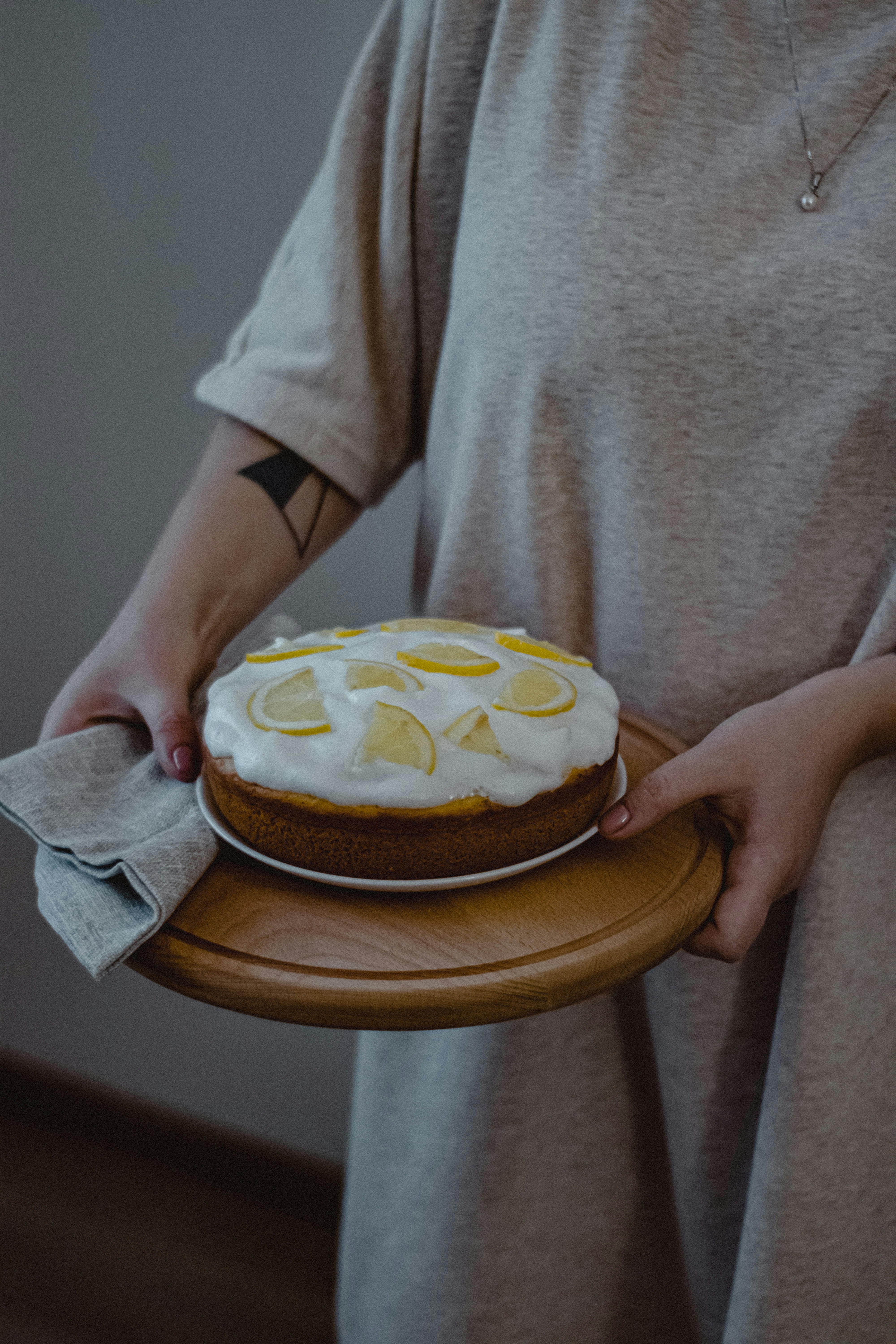 Lemon-glazed cake on a wooden pedestal held by a softly dressed figure