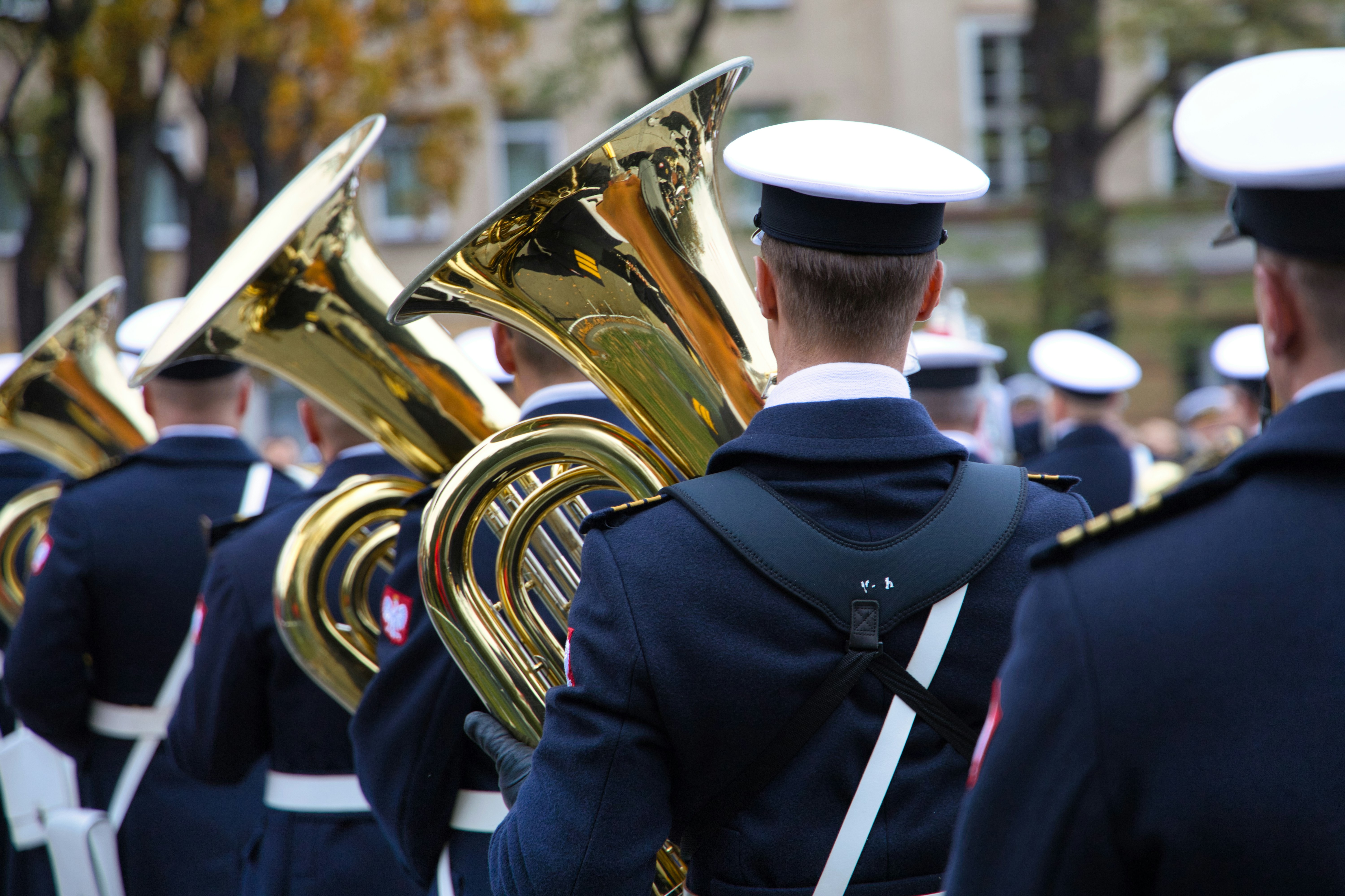 Marching band members in navy uniforms play brass instruments during a parade.