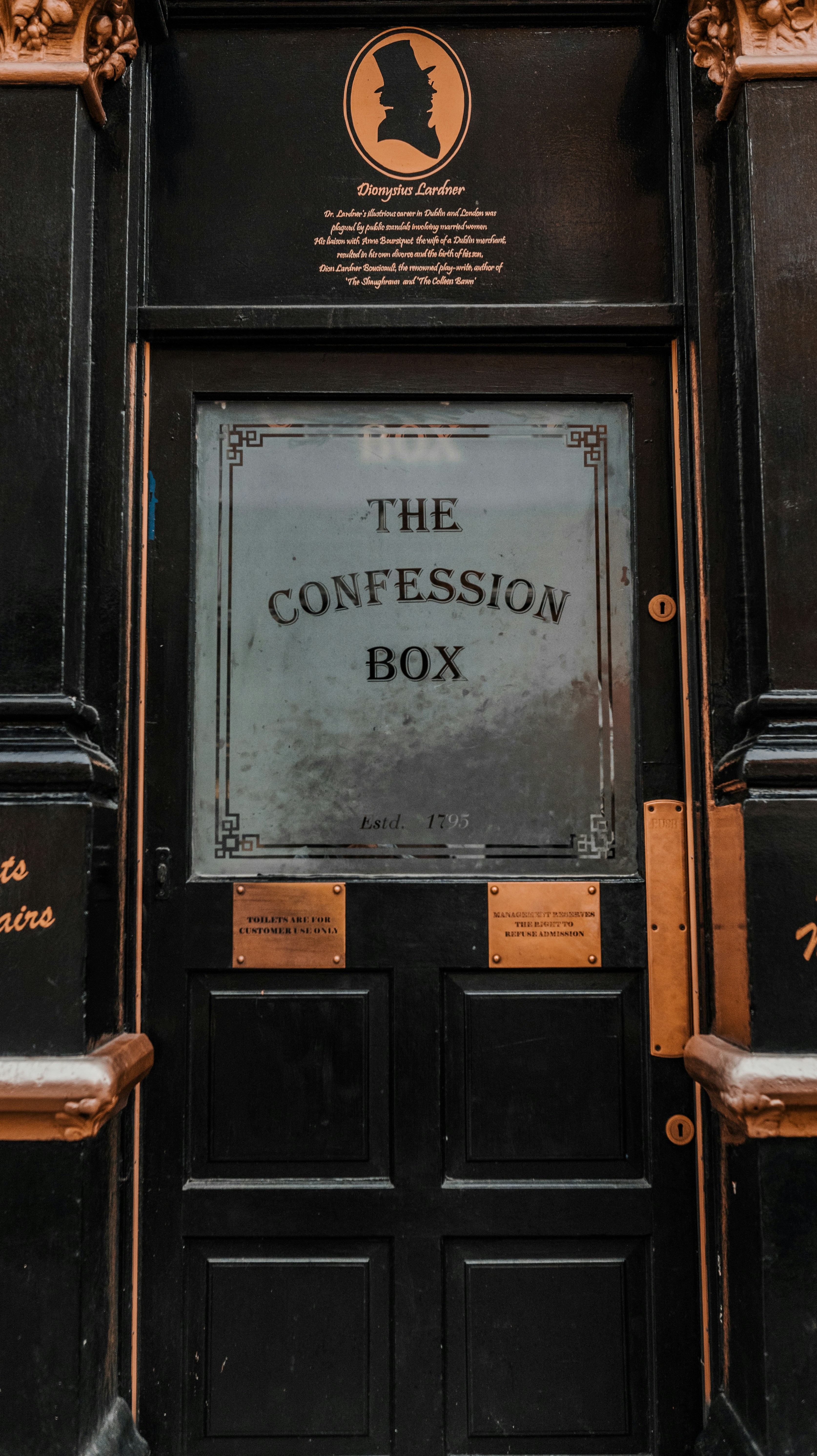 Intricately designed door featuring the words 'THE CONFESSION BOX' and a silhouette above, hinting at its historical significance. Established in 1795.