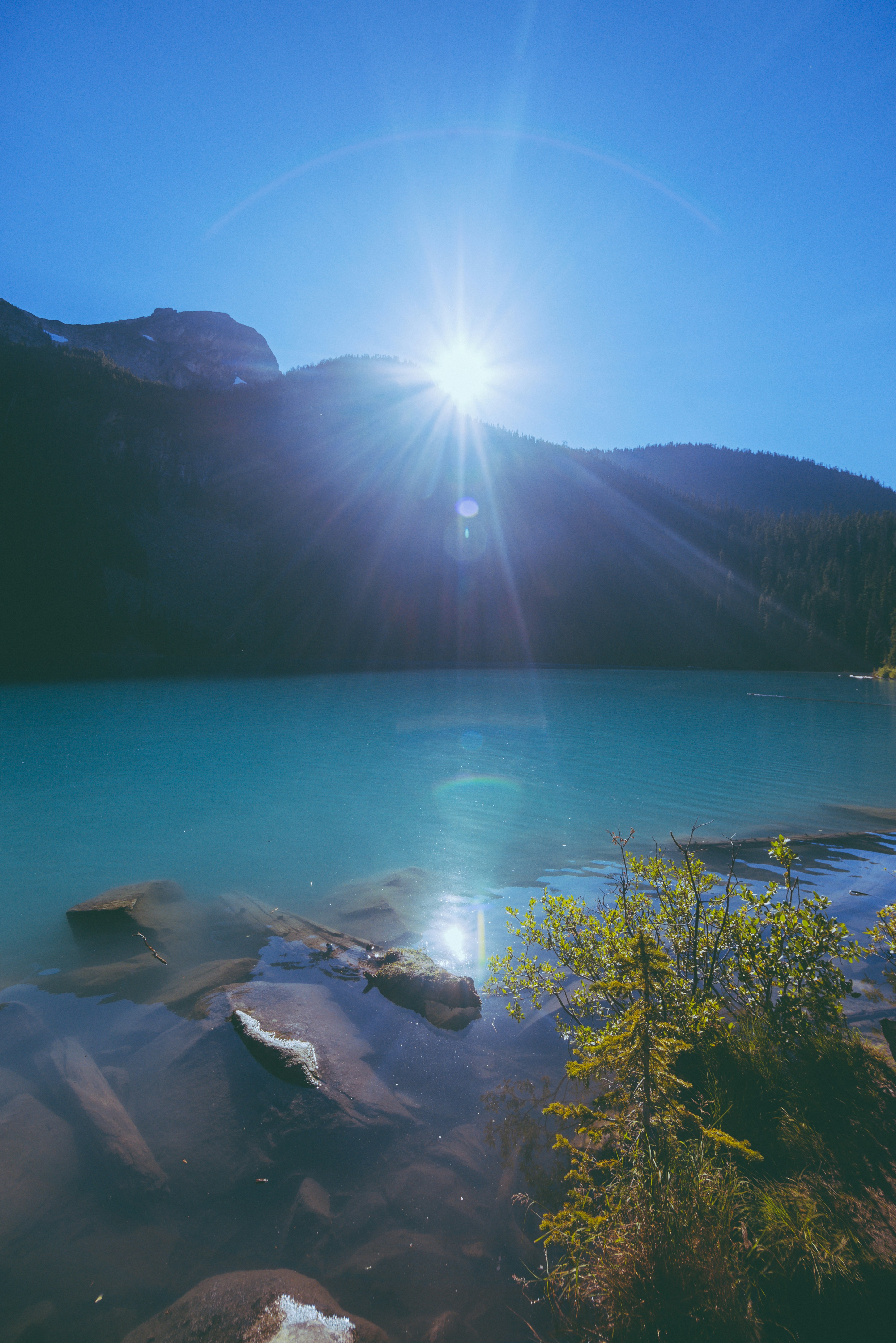 Sunburst over turquoise alpine lake framed by pine-clad peaks