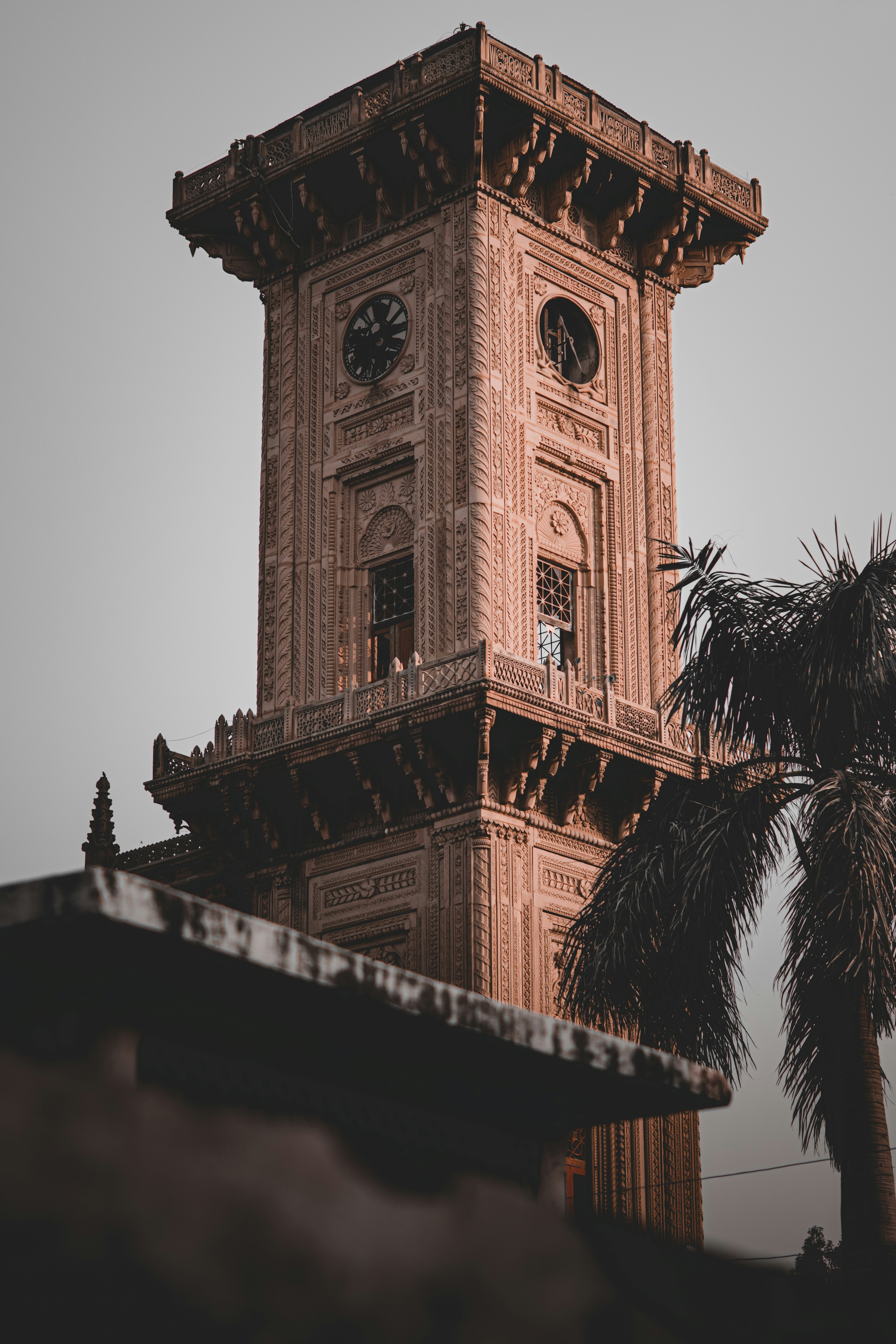 Dusk-tinged Clock Tower: Intricate Stonework Rises Over Palm Fronds