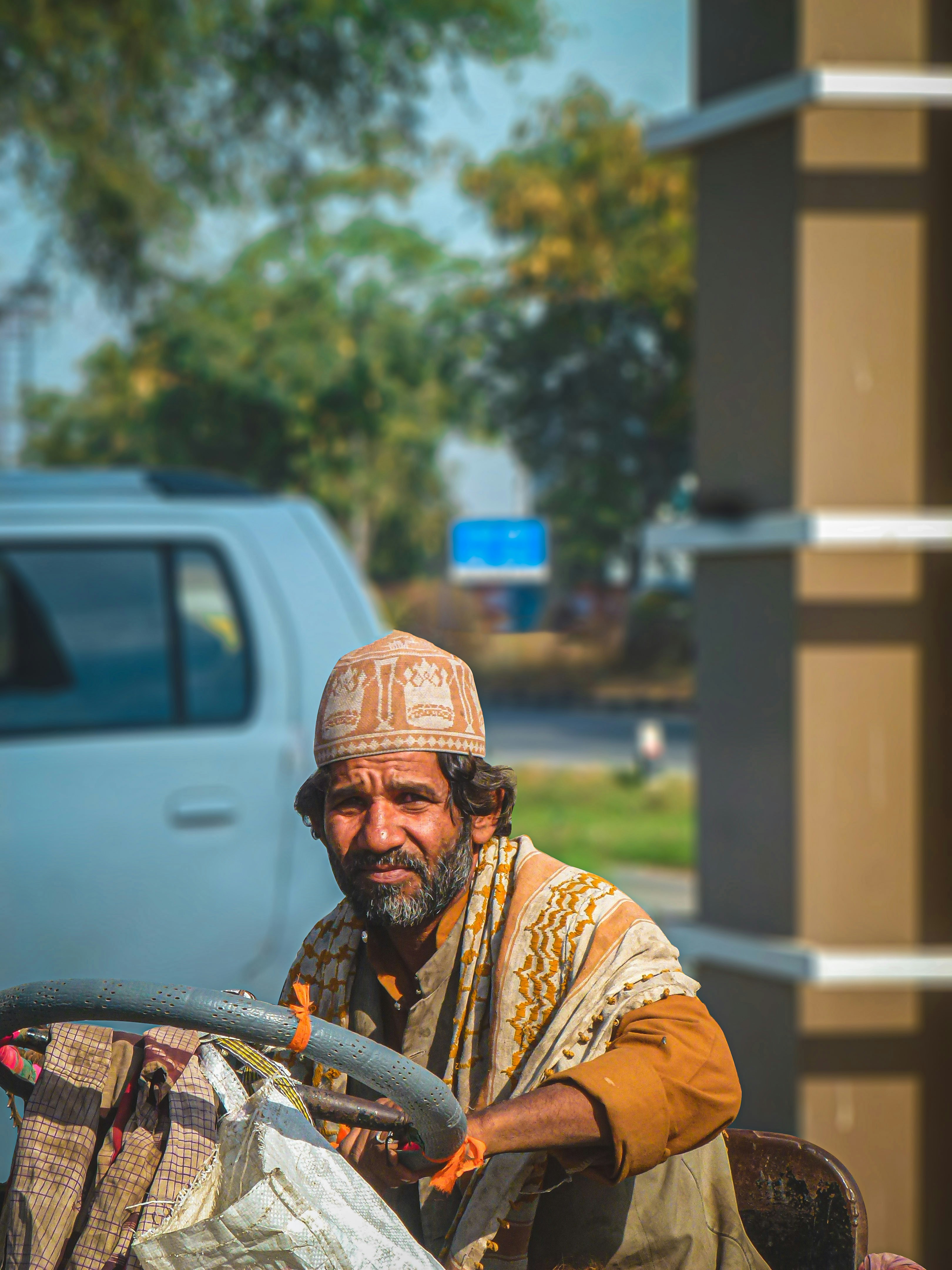 A candid street portrait of a man in traditional attire seated on a bicycle, with a softly blurred urban backdrop.