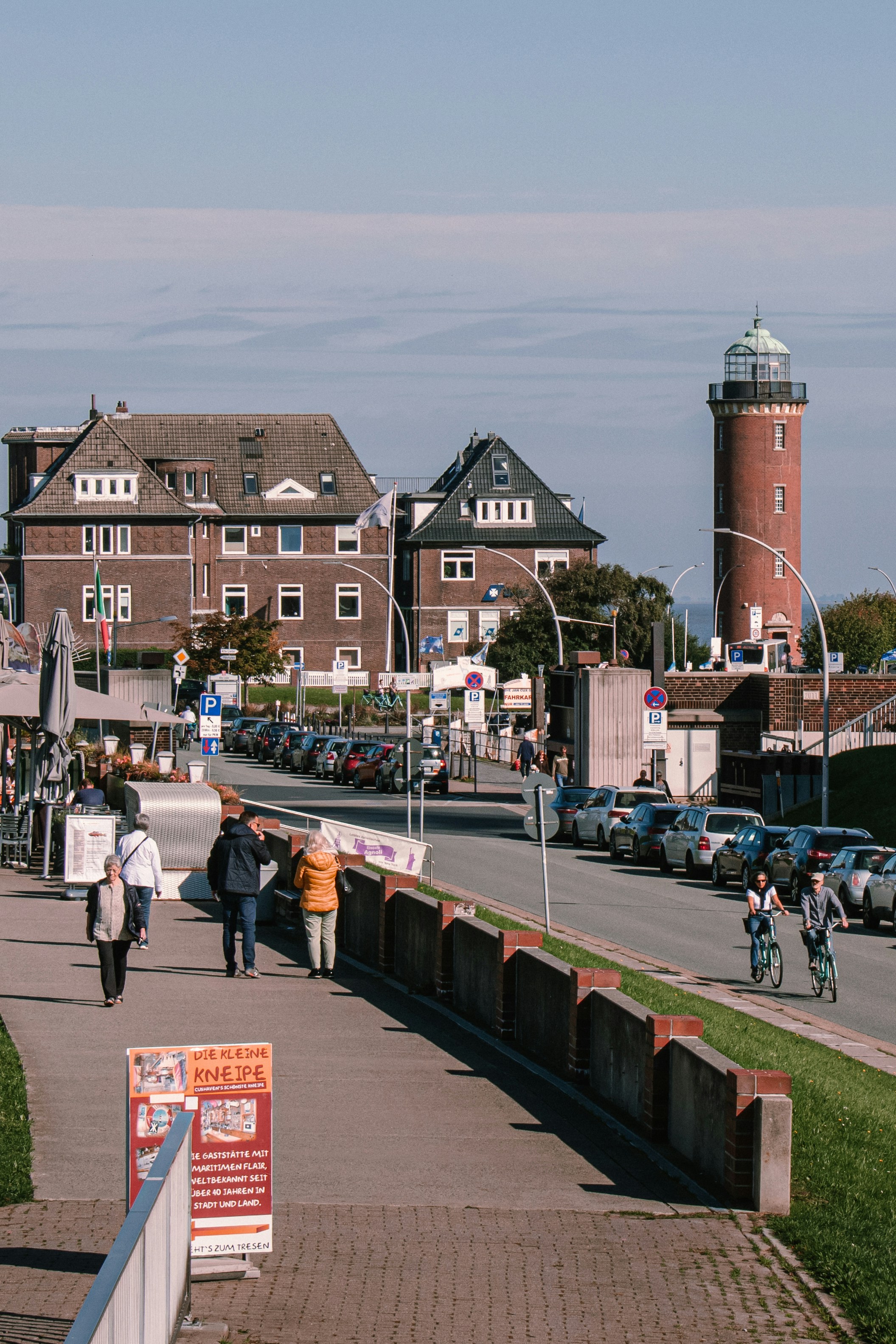 a group of people walking on a sidewalk next to a road with cars and buildings