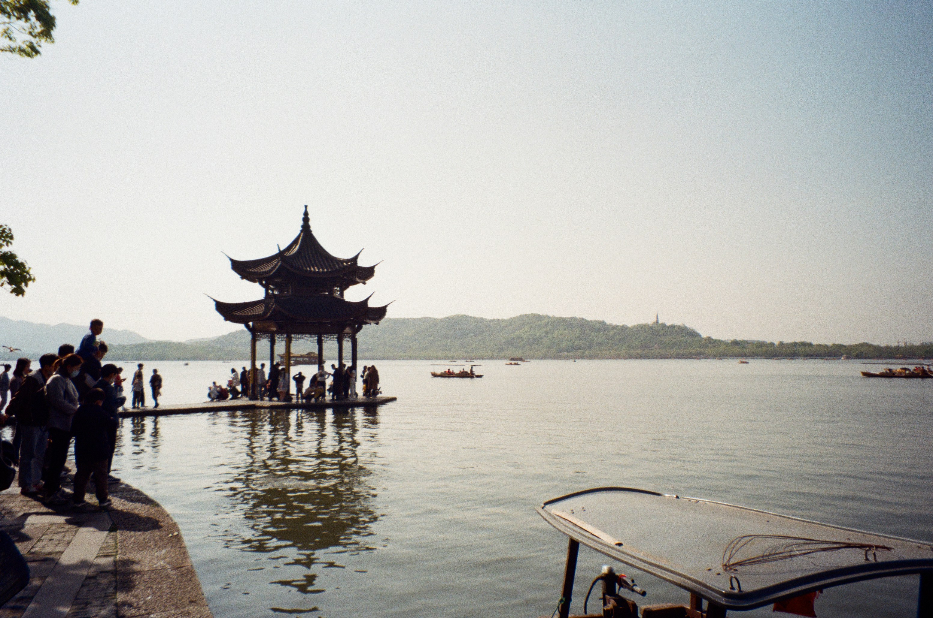 a group of people standing on a dock by a body of water with West Lake in the background