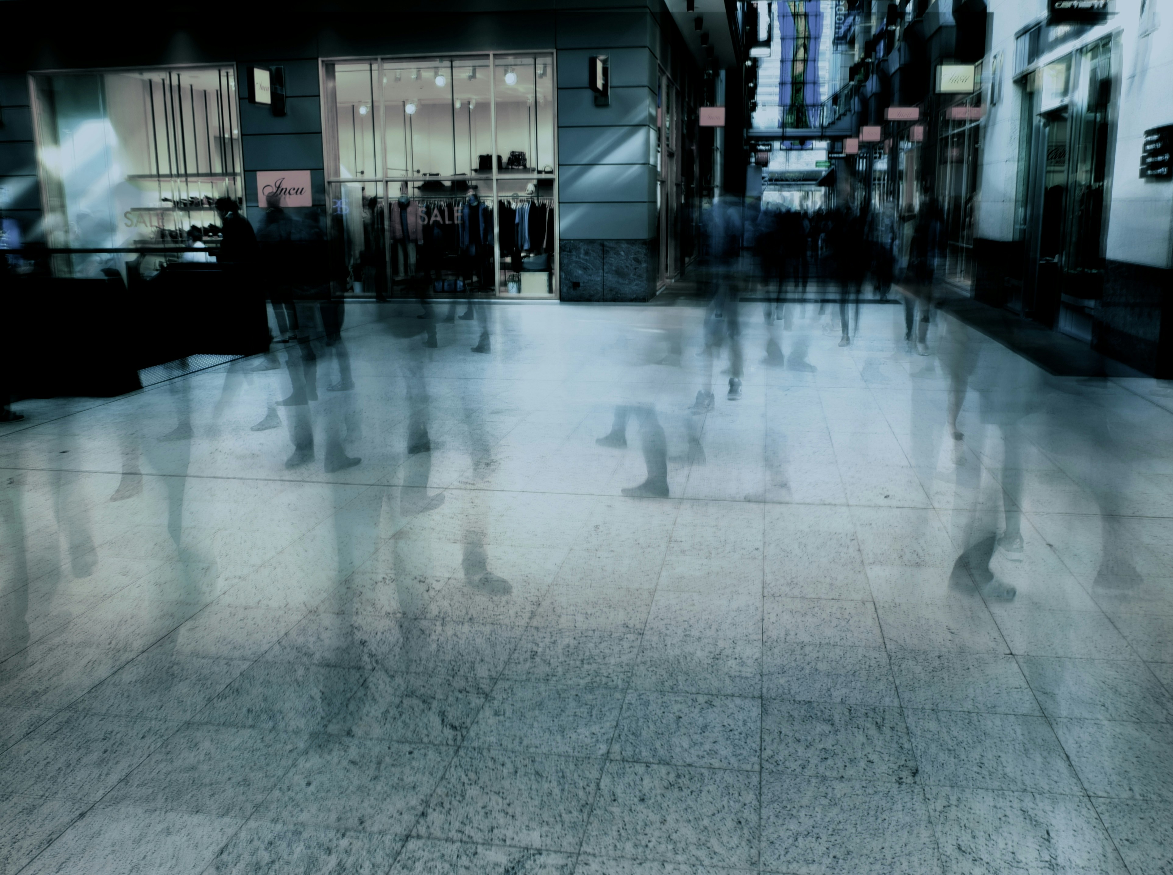 Blurred figures moving through a bustling shopping arcade, capturing the essence of urban motion. The scene conveys a sense of dynamic energy and anonymity.