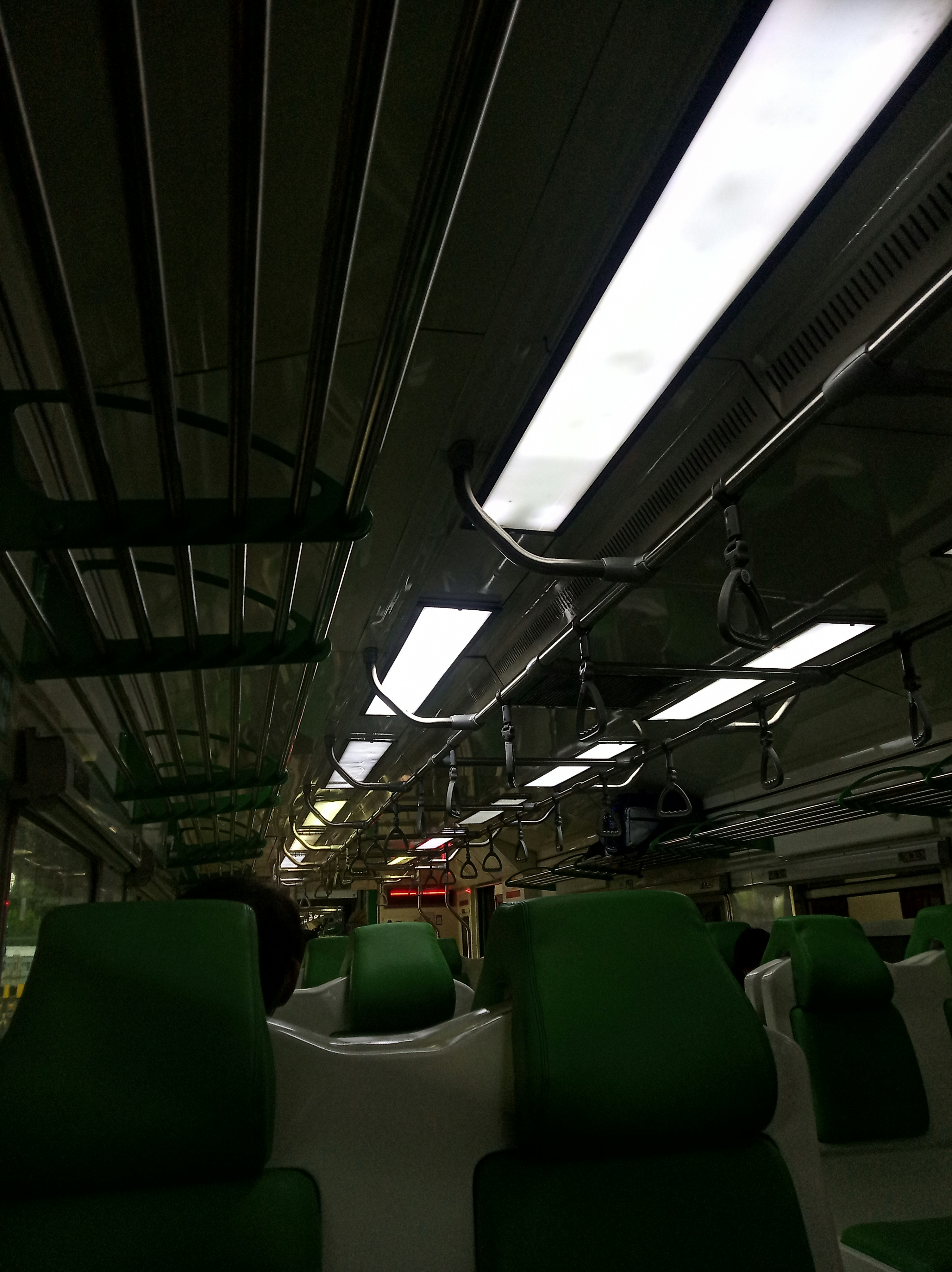 Interior of a modern train featuring green seating and overhead lights, capturing the essence of daily commuting. The design emphasizes functionality and comfort.