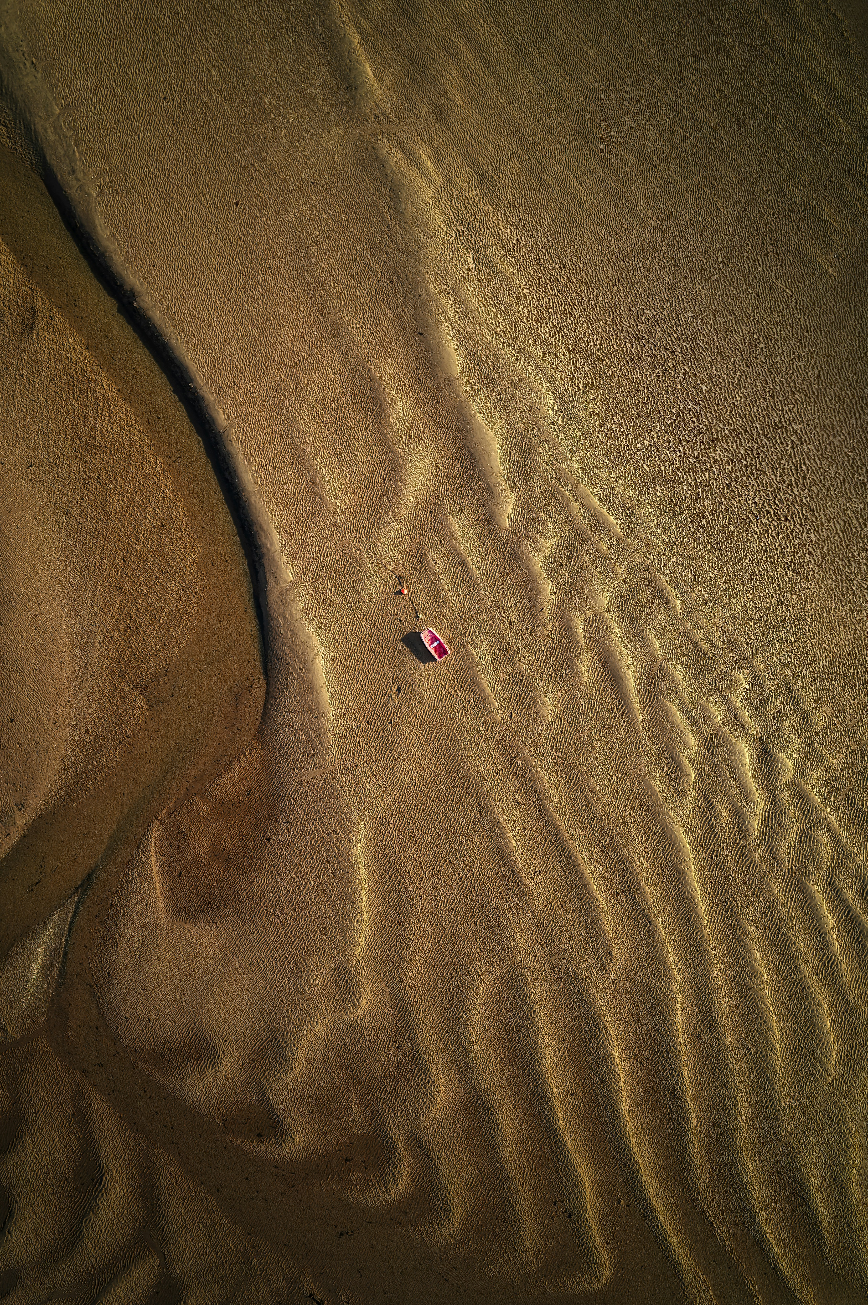 A lonesome boat in tide carved dunes and shadows of the Exe Estuary, Devon, UK