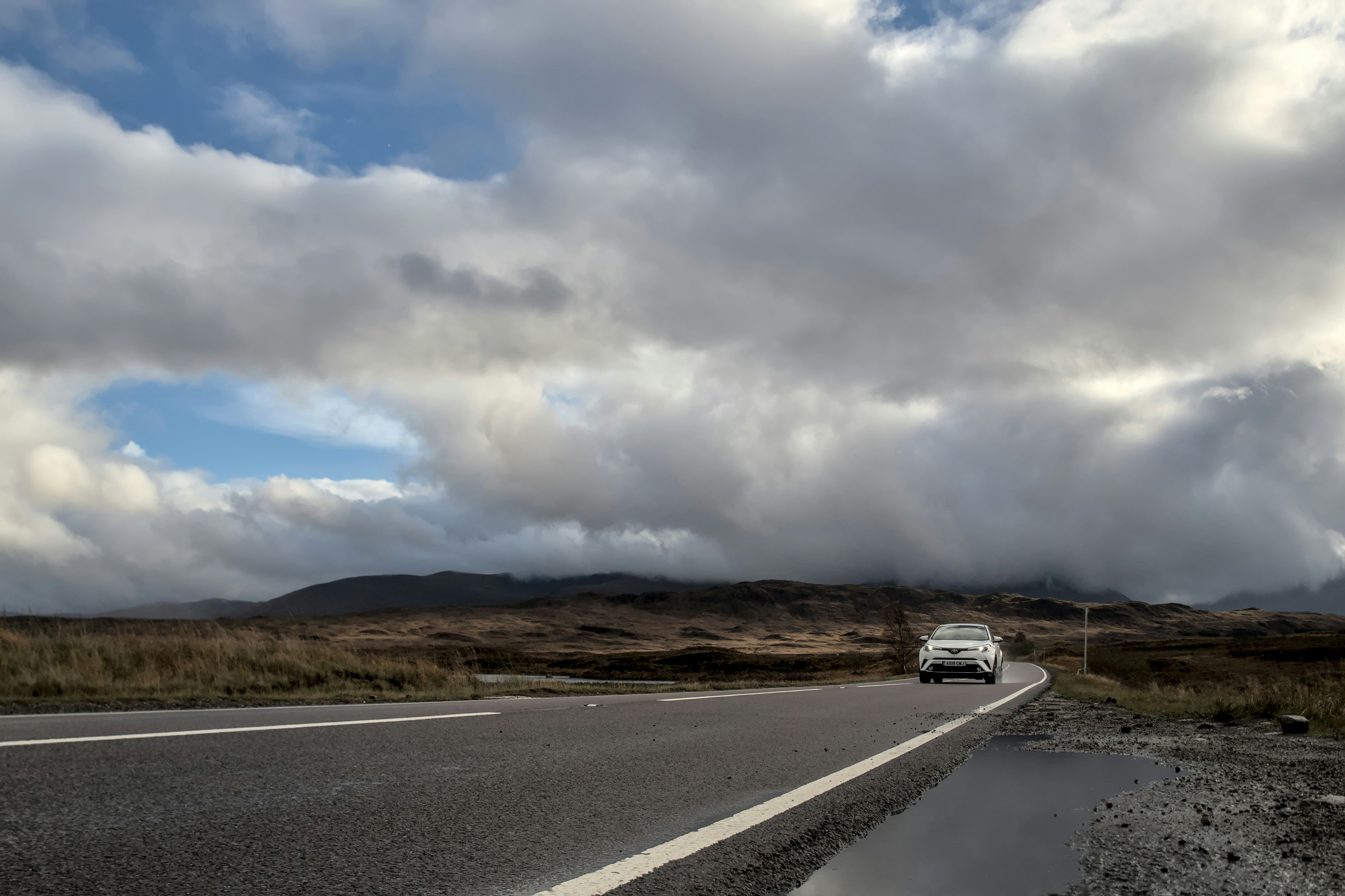 White Car on a Winding Desert Road Beneath Storm-Cloud Skies