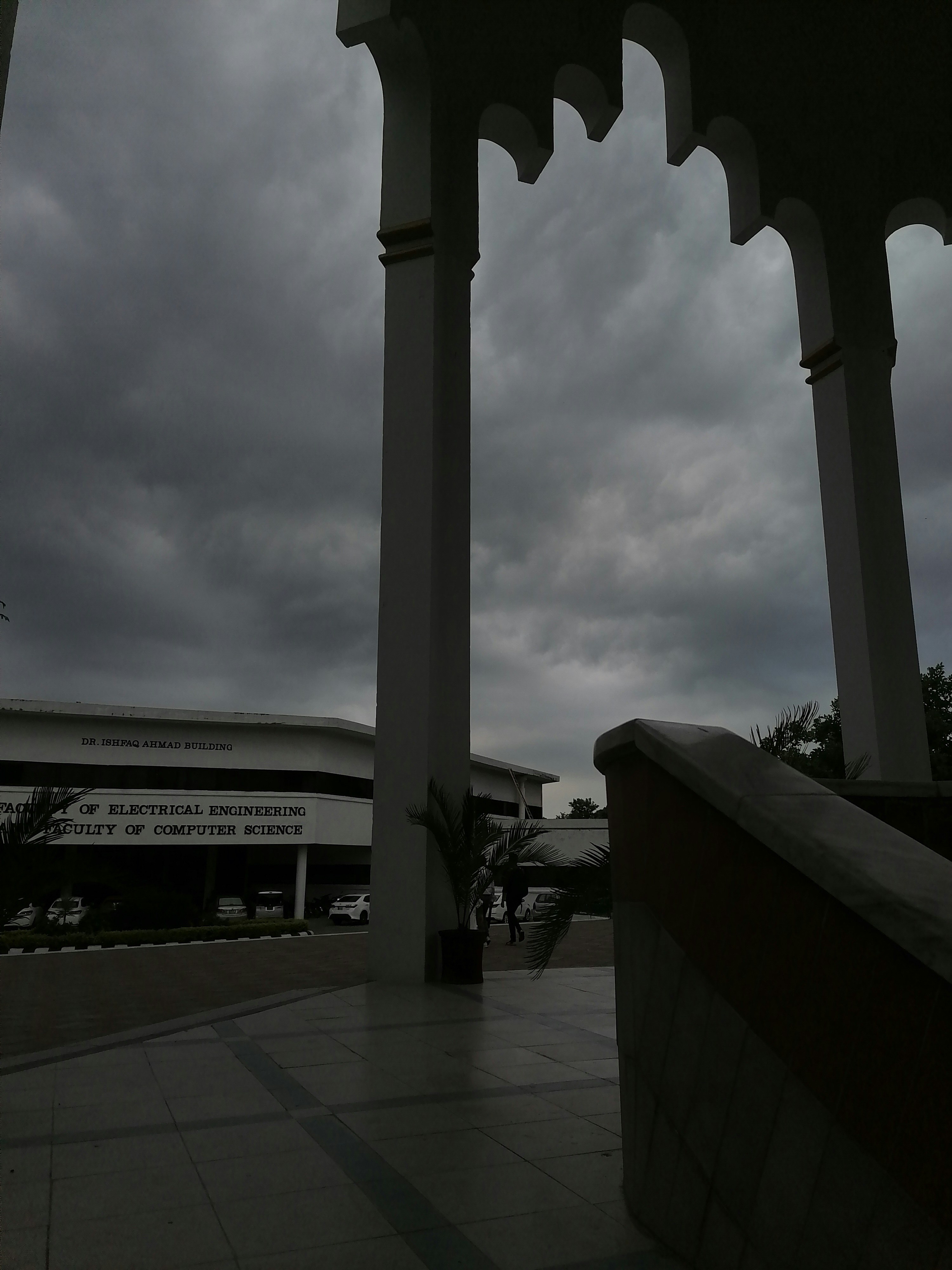 Majestic columns frame a view of a university building under a cloudy sky, creating a dramatic atmosphere. The scene captures the essence of academic architecture.