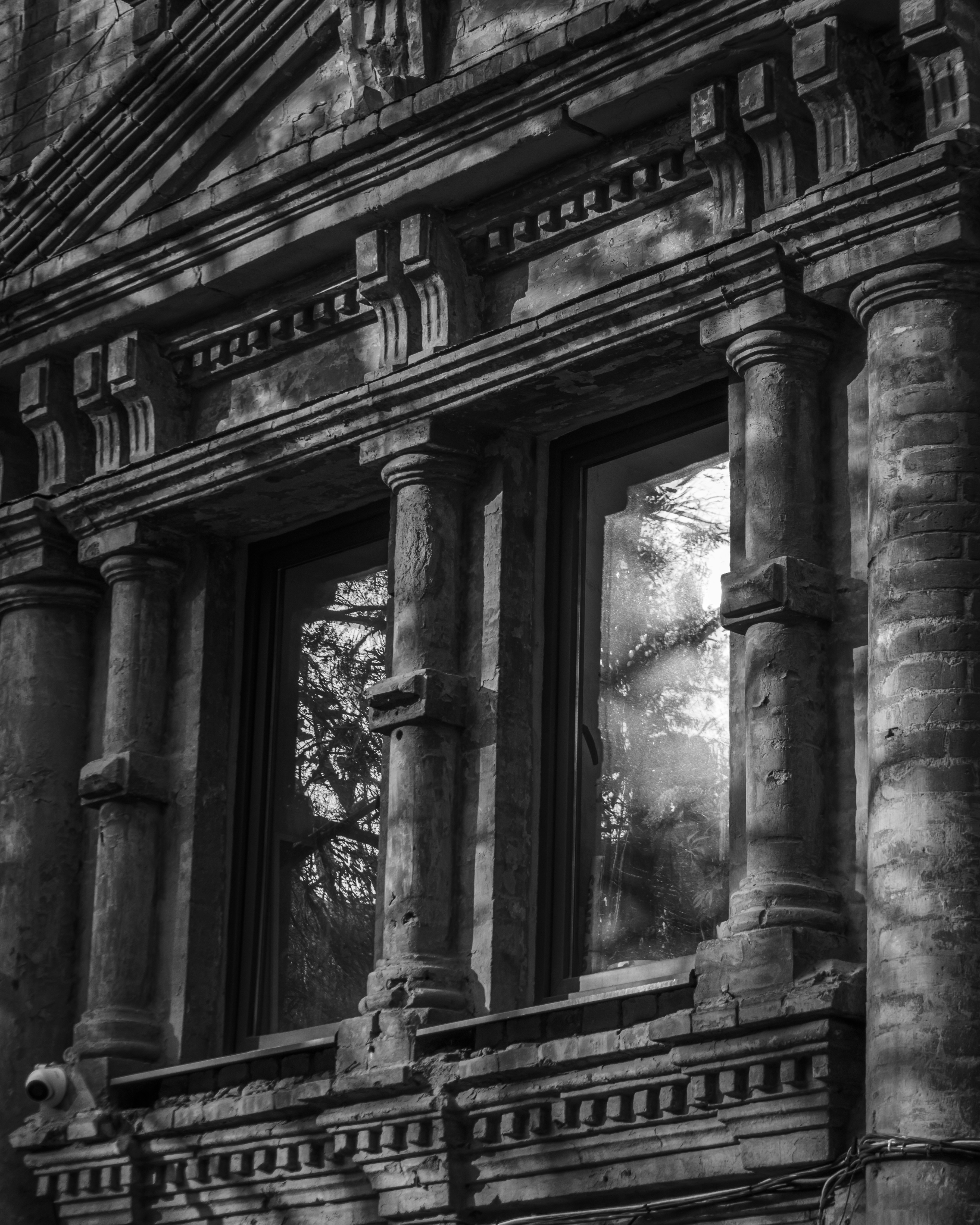 Intricate brickwork and columns frame two reflective windows, showcasing the interplay of light and shadow. The aged facade tells a story of time and craftsmanship.