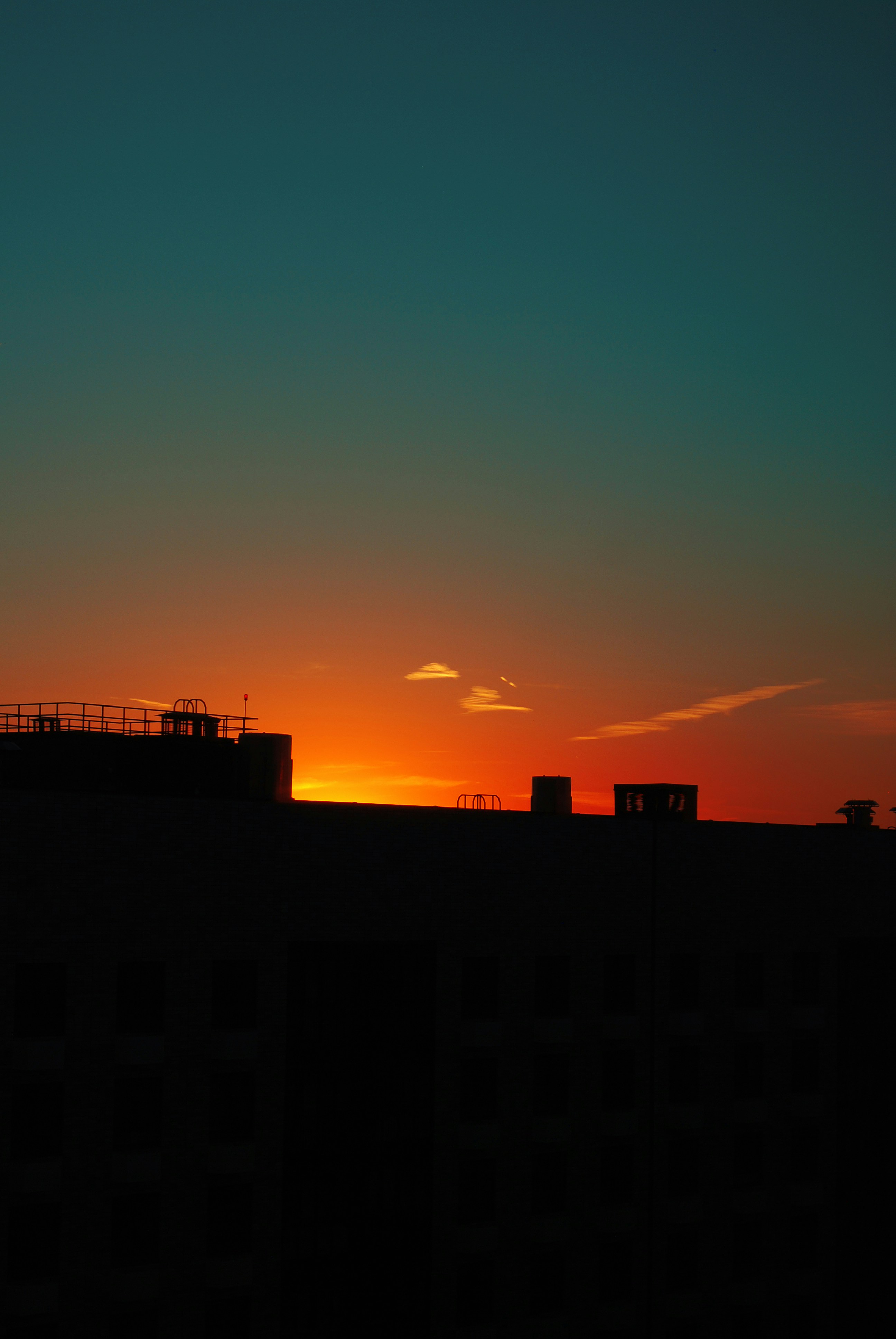 Silhouette of a building against a vibrant sunset, showcasing a gradient of orange and blue hues in the sky. The scene captures the transition from day to night.