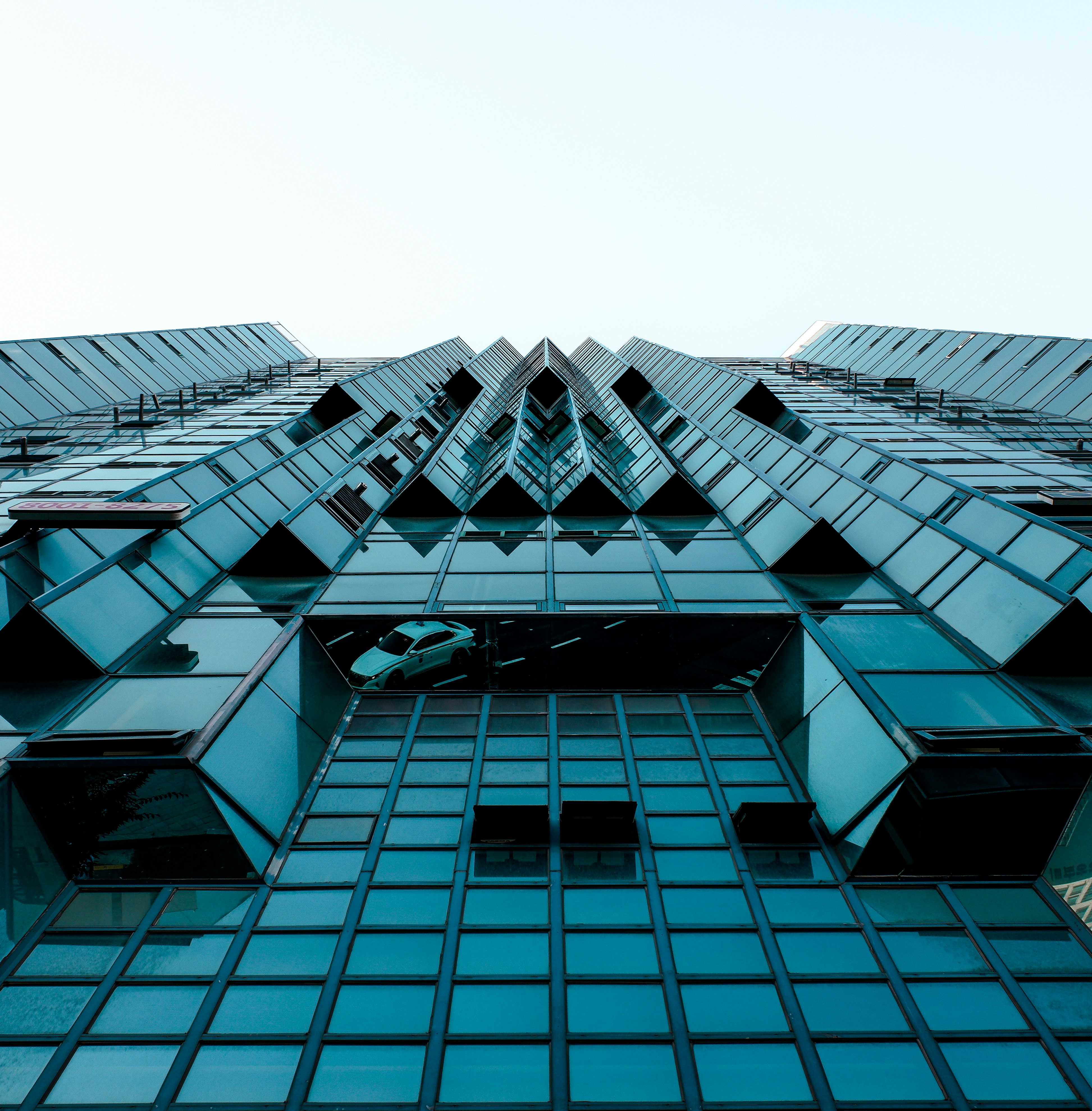 Photograph of a modern glass tower seen from ground level. Facades converge toward a diamond-shaped apex, highlighting strong geometric symmetry.