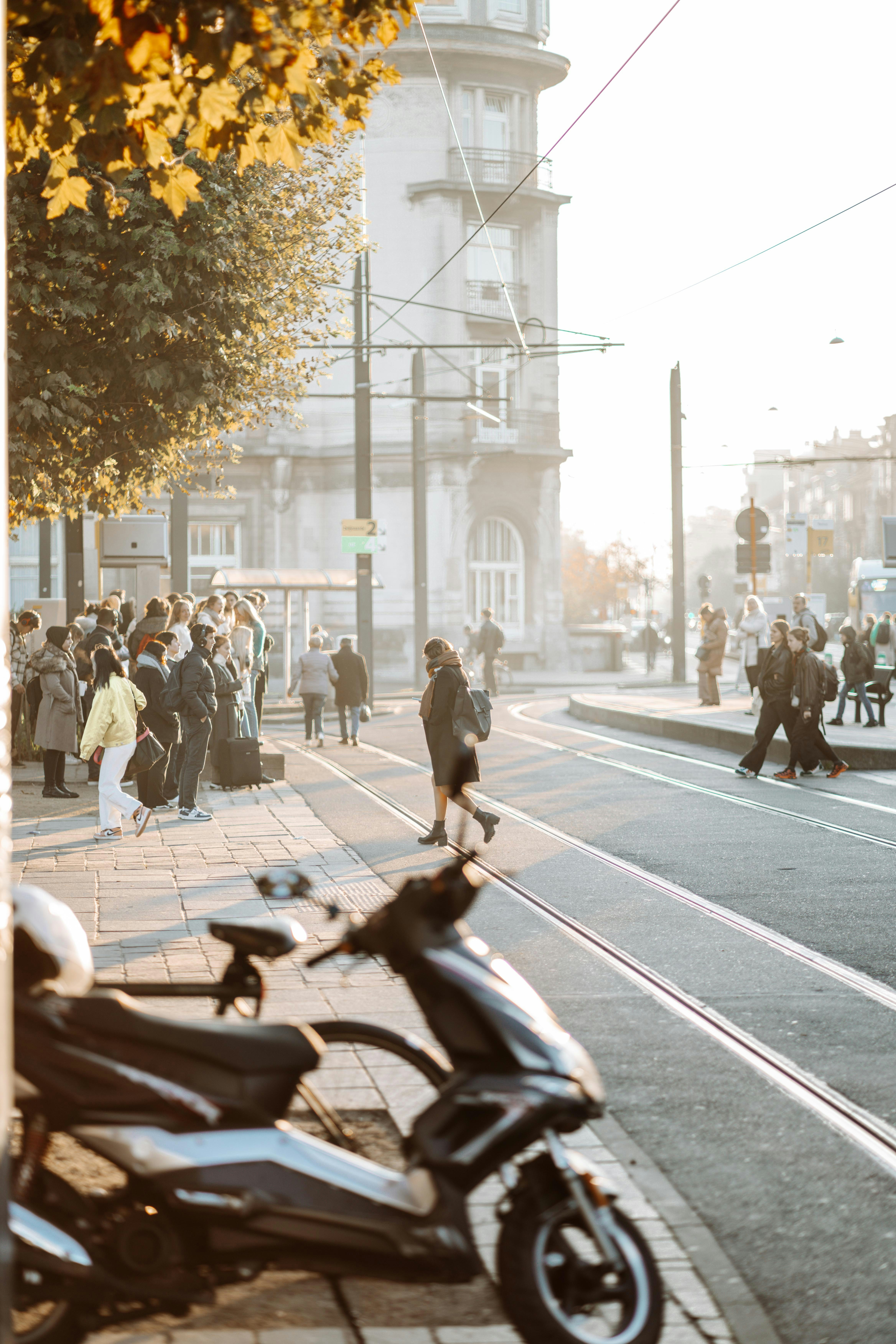 Golden Hour Crossing: Pedestrians, Rails, and a City Scooter