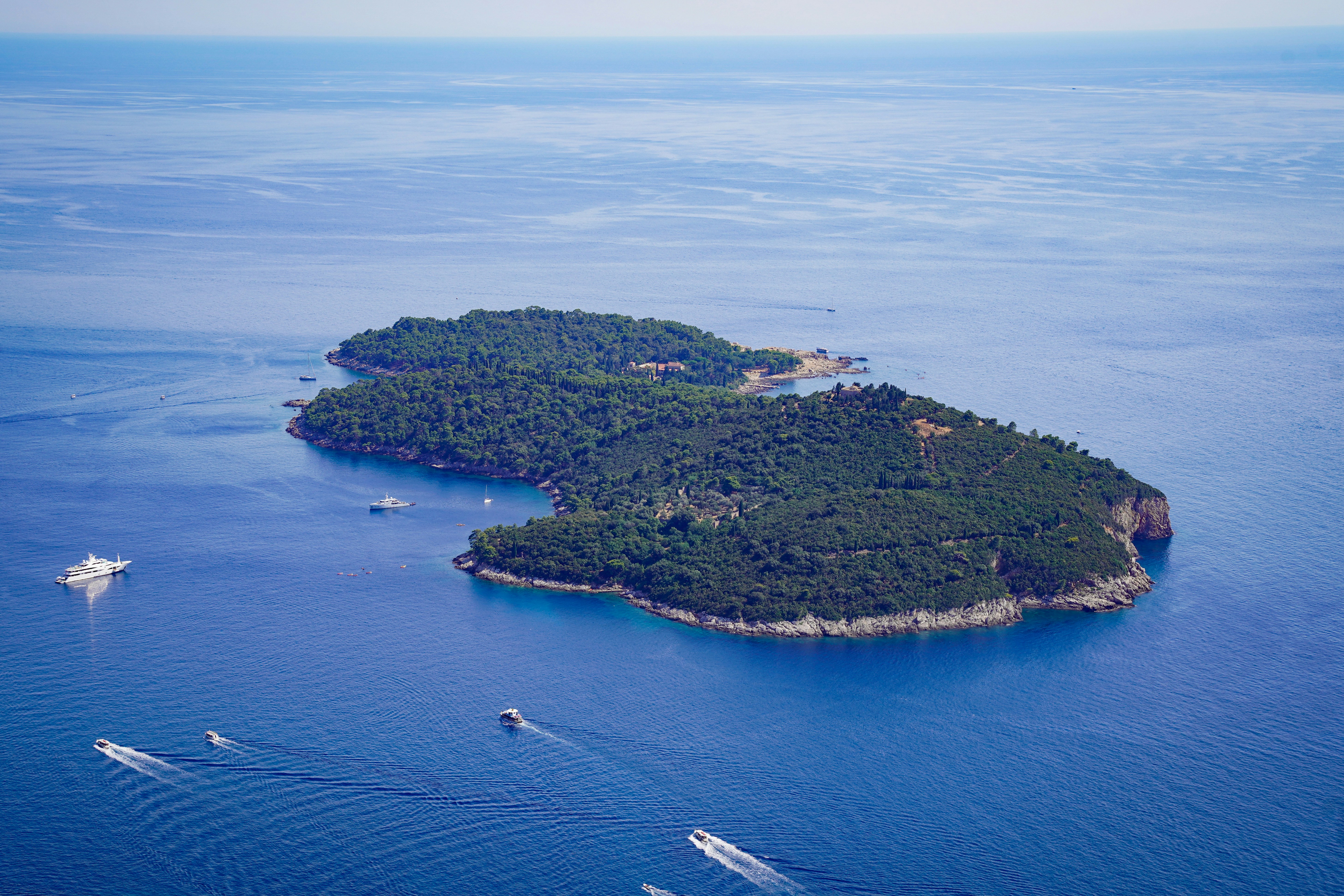 Aerial view of a lush green island surrounded by azure waters, with boats gliding nearby. The image captures the tranquil essence of coastal nature.