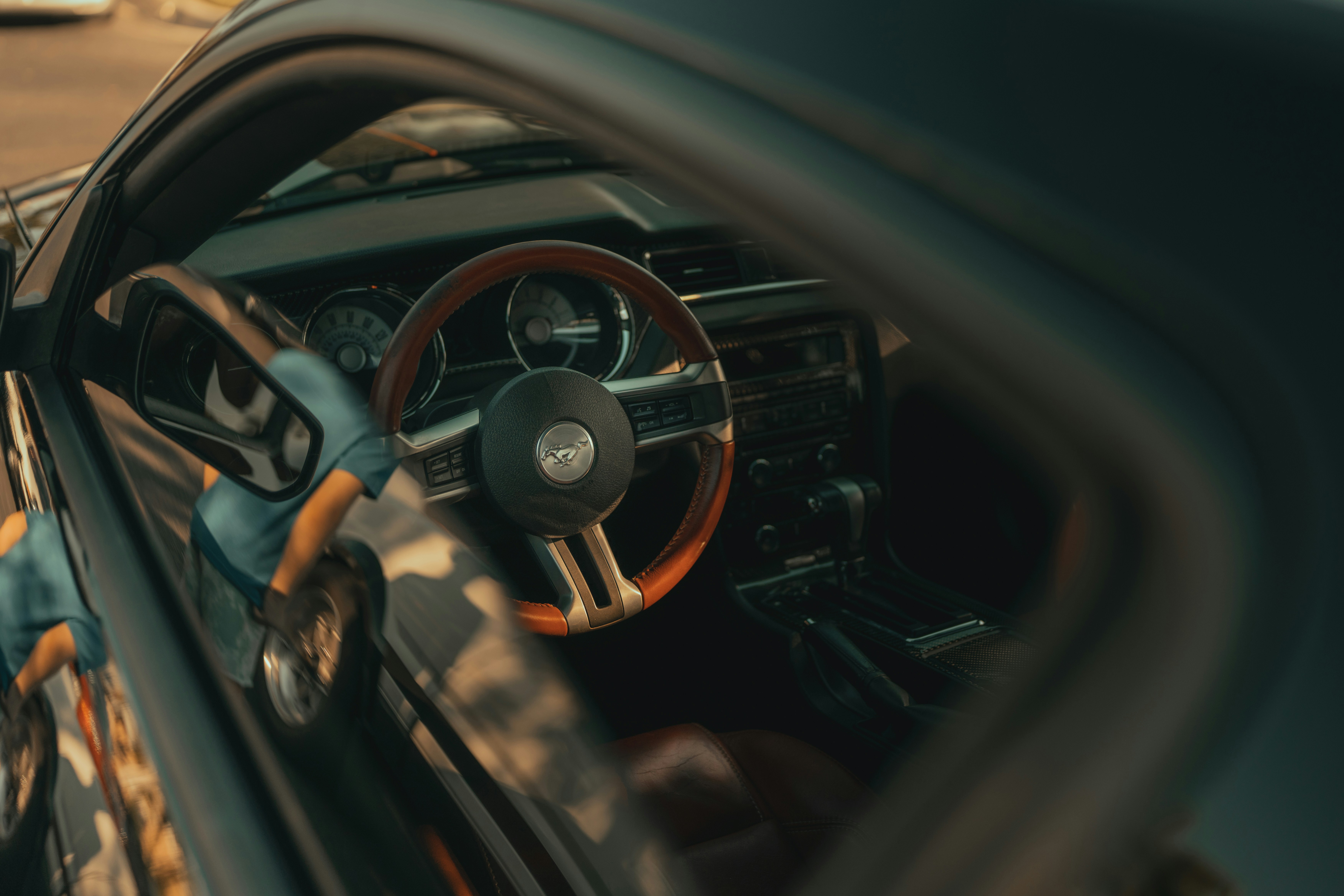 Interior view of a sleek car showcasing a wooden steering wheel and dashboard, with reflections hinting at the outside environment.