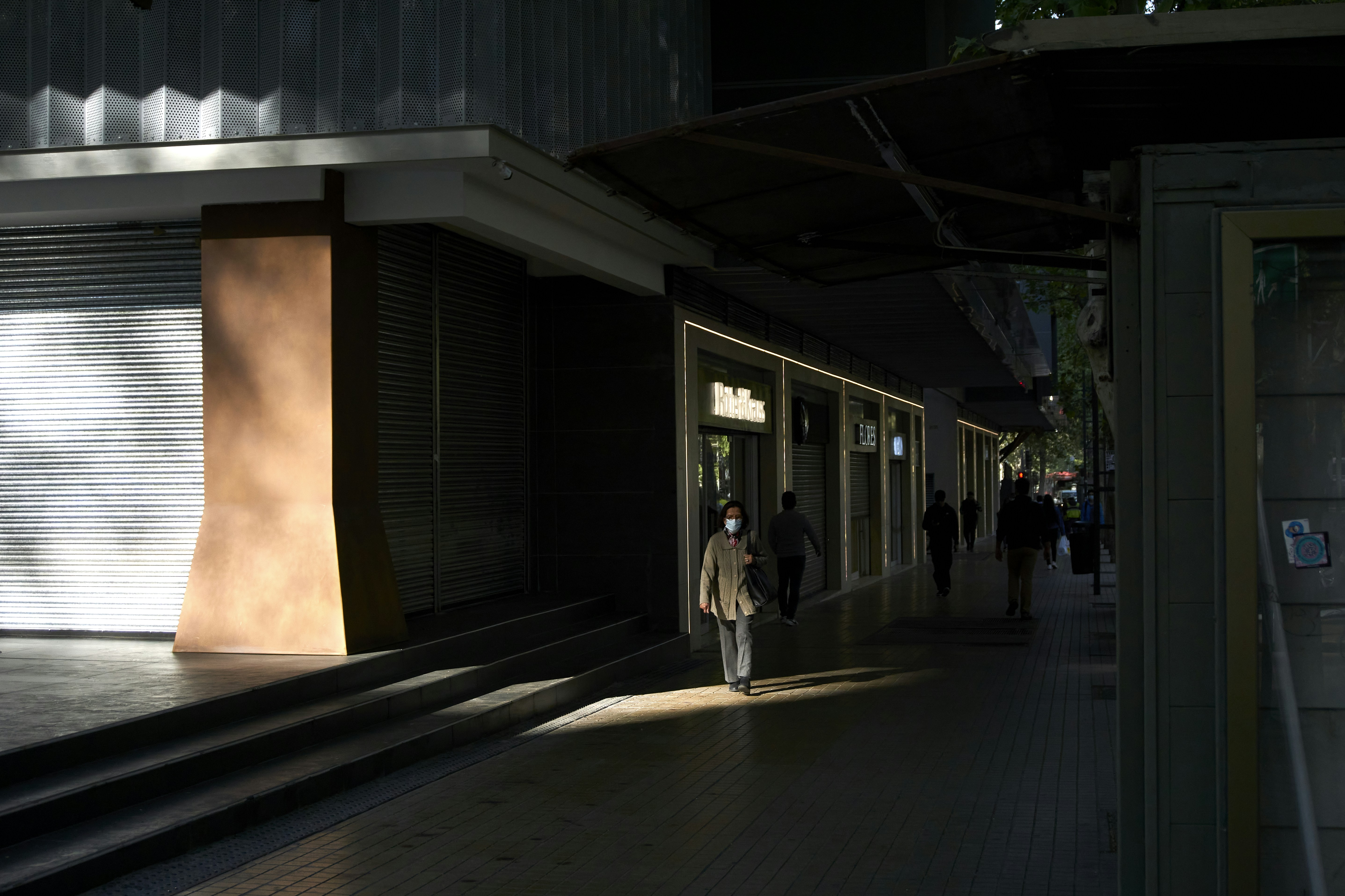 Dimly lit urban alley with a person walking through a sunlit patch among shadows.
