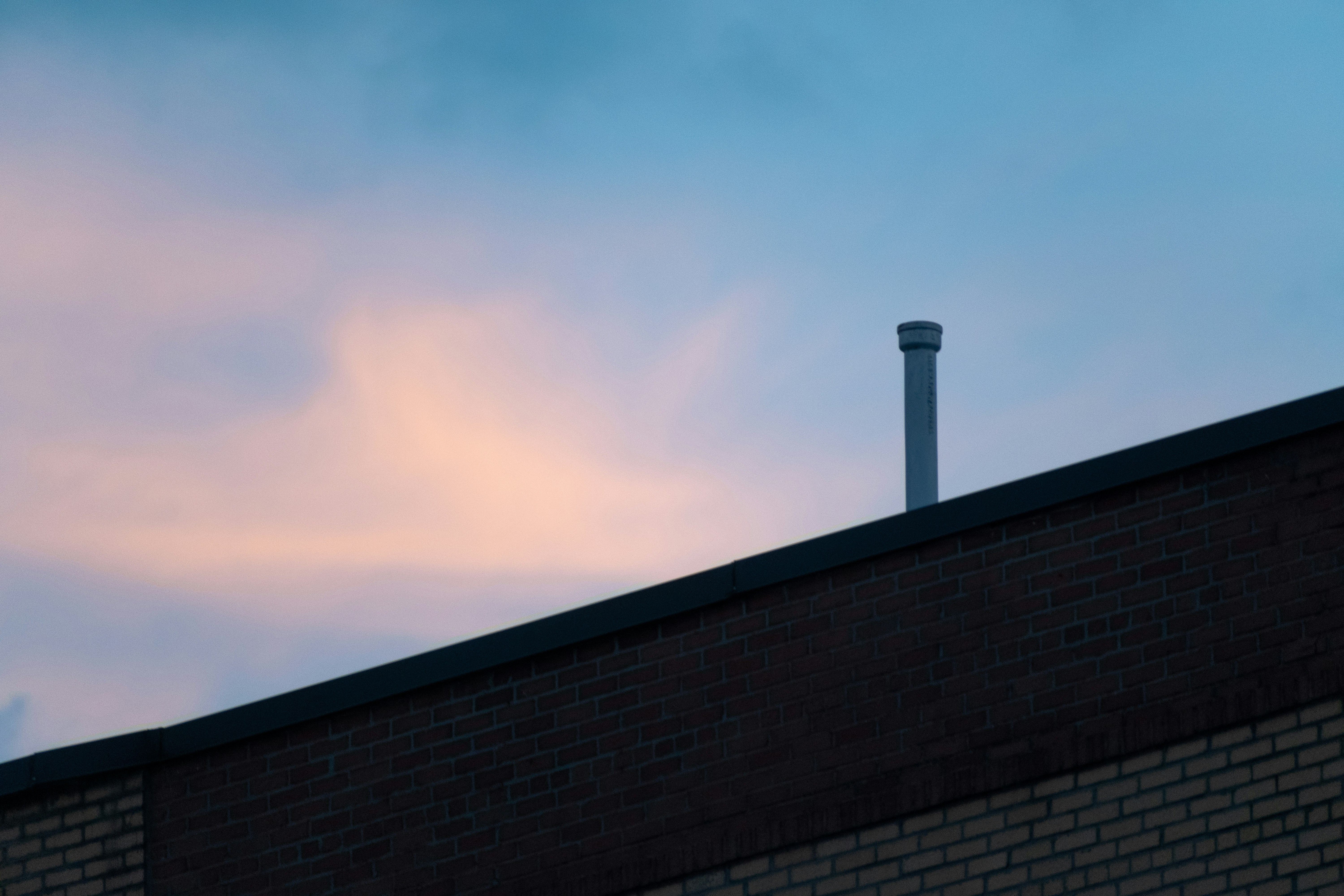 Dusk on the Brick Roof: A Lone Vent Against Peach Sky