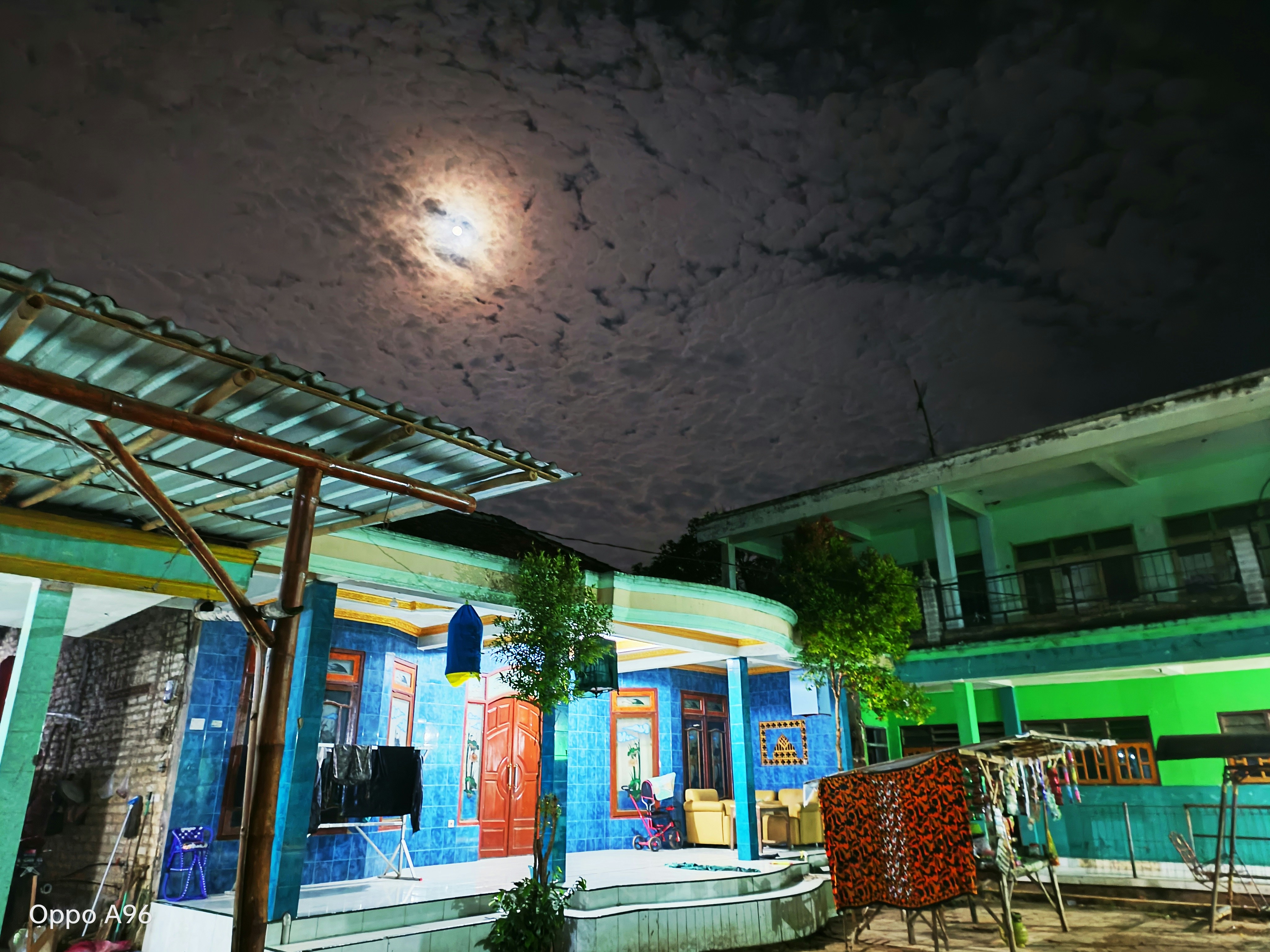 A tranquil courtyard illuminated by the moon, featuring colorful buildings and hanging laundry. The scene captures the peaceful ambiance of nighttime in a residential area.
