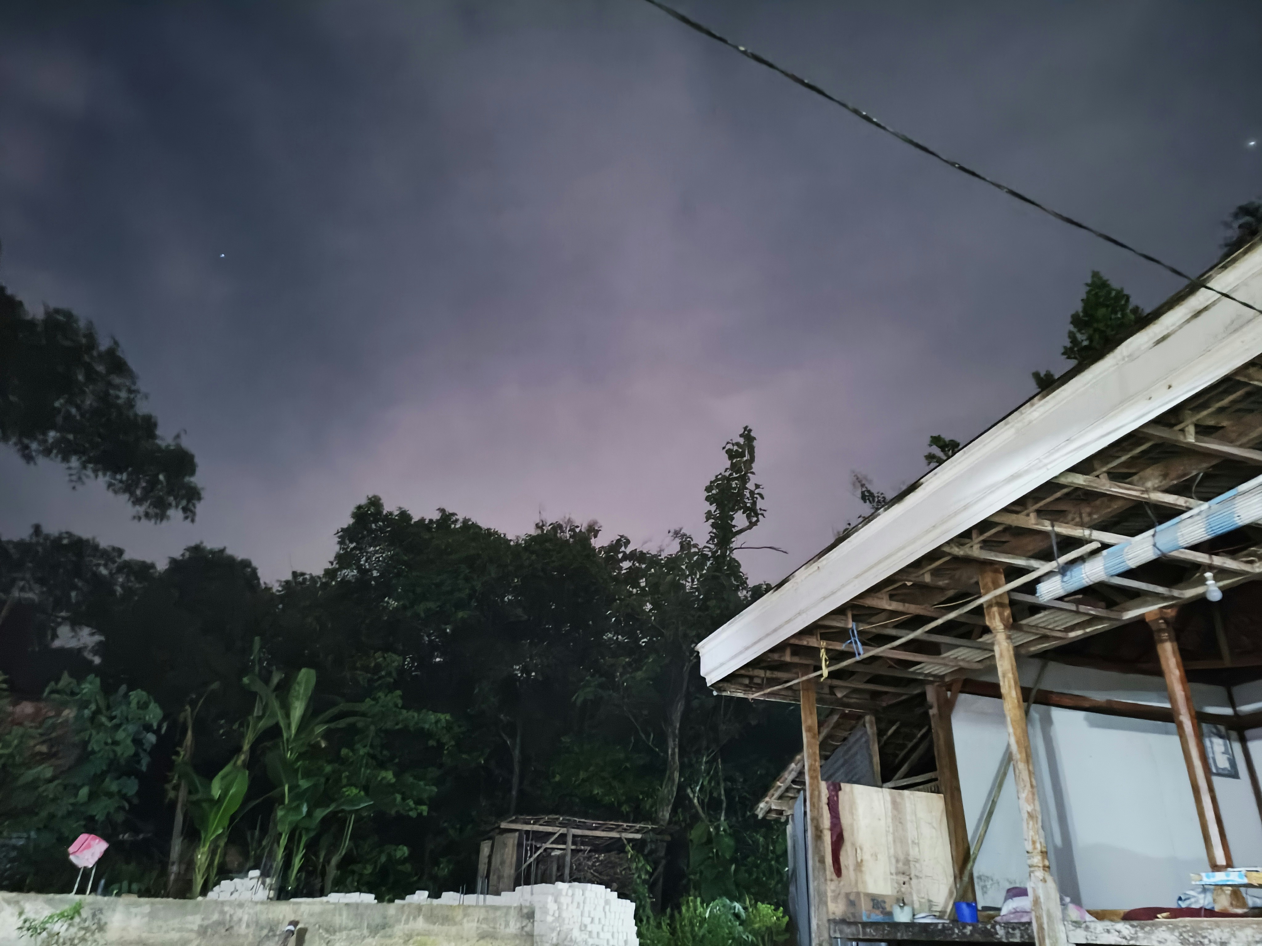 Dusk scene with a wooden building on the right and a purple-tinged sky above dense forest.