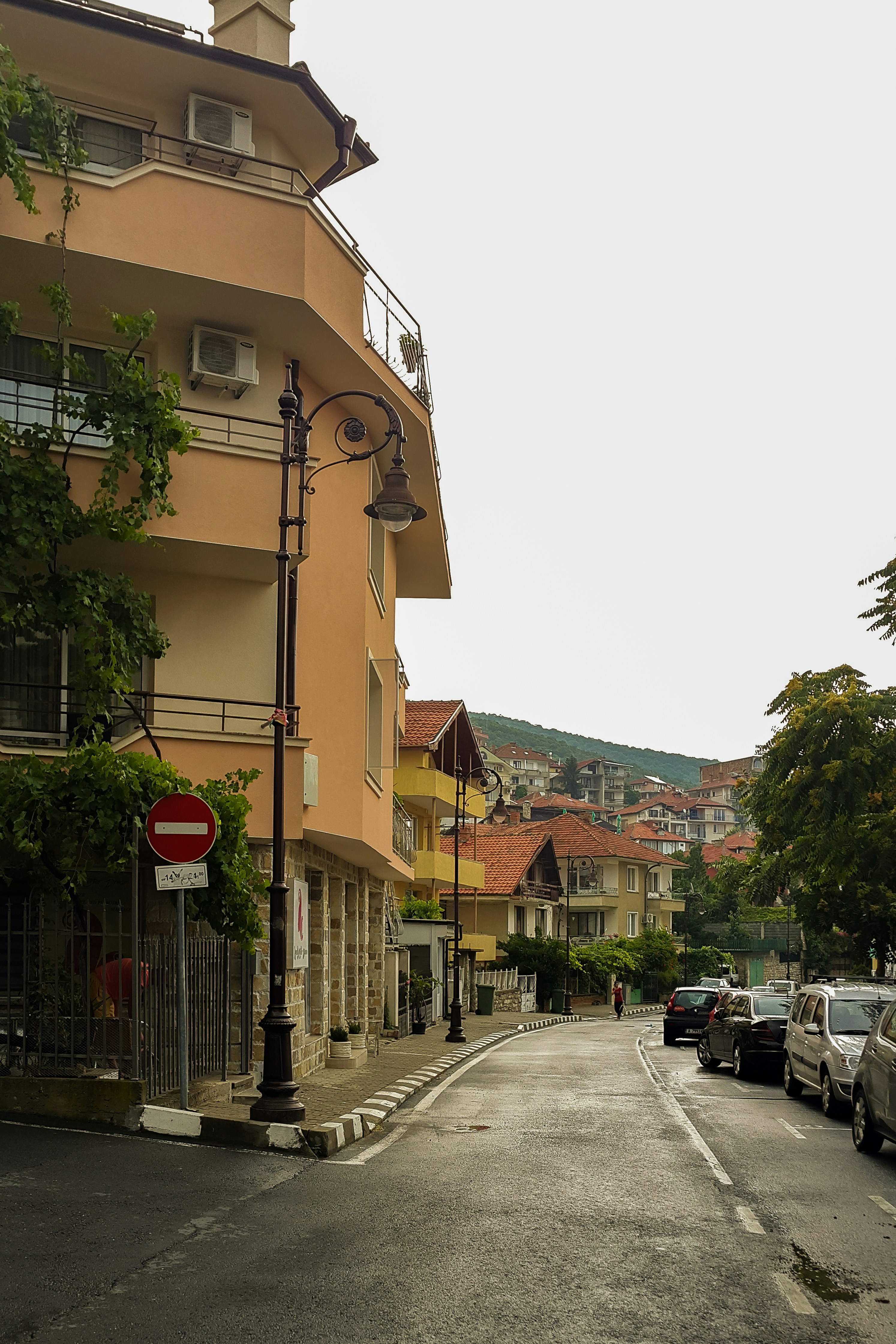 Charming street scene featuring colorful buildings and a winding road, set against a backdrop of hills. A no-entry sign adds to the urban narrative.