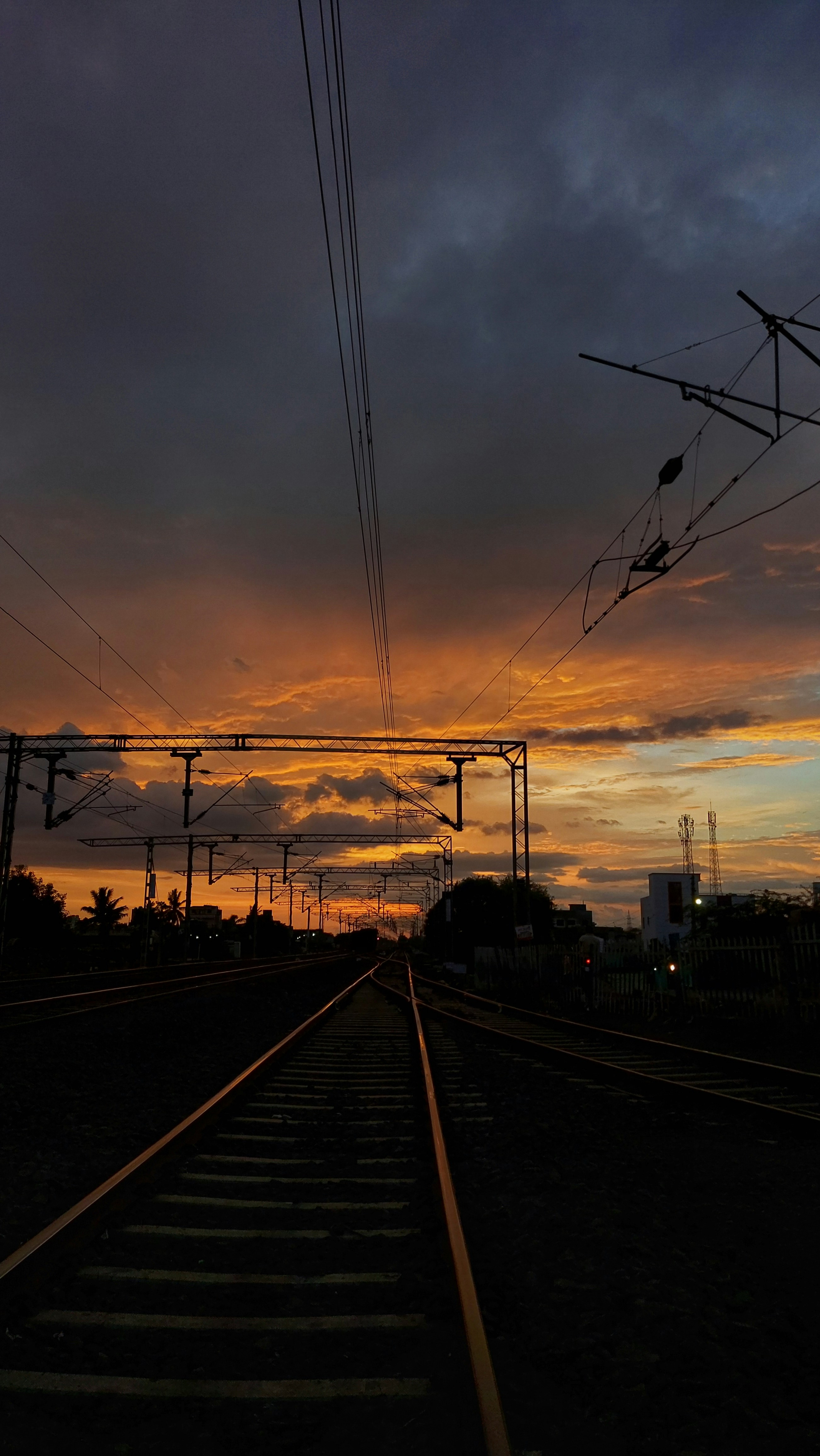 Sunset glow washes the railway lines and overhead wires, pushing the eye toward the distant horizon. This photograph captures industrial silhouettes against a vibrant sky.