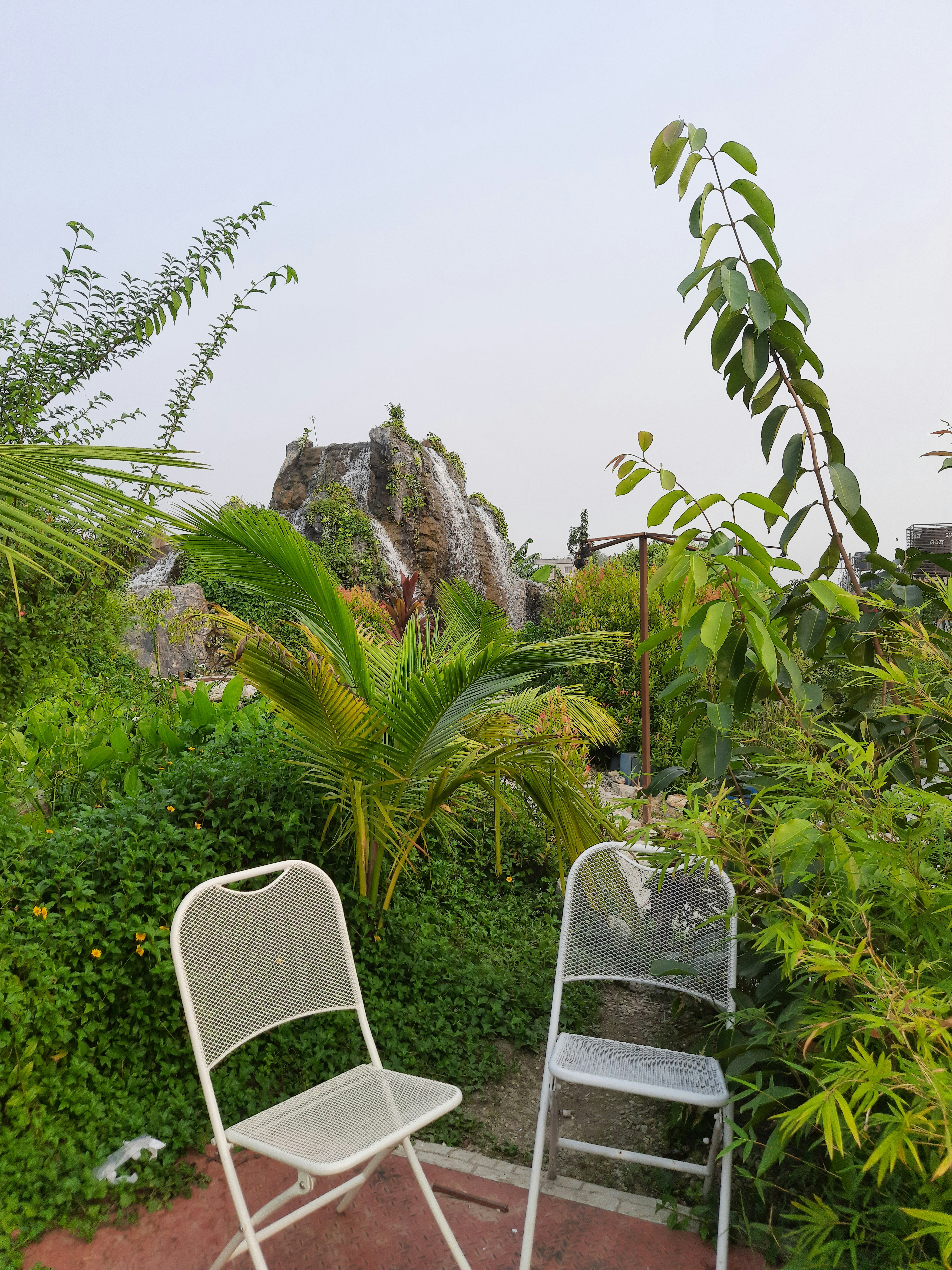 Two empty chairs surrounded by lush greenery and a rocky backdrop with cascading water, inviting moments of relaxation and contemplation.