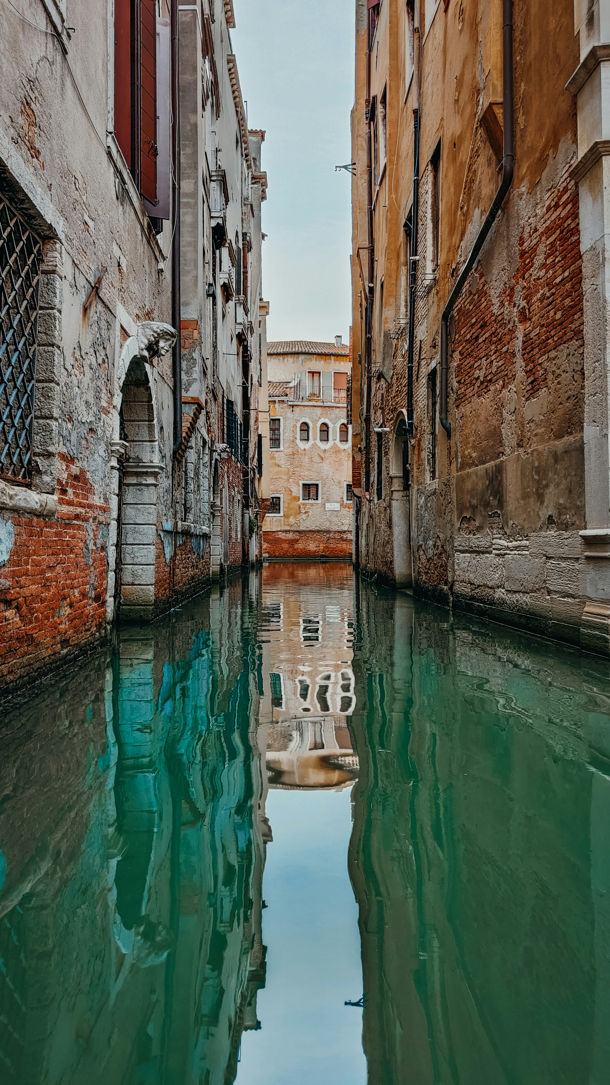 Narrow canal flanked by historic buildings, with reflections shimmering on the water's surface.