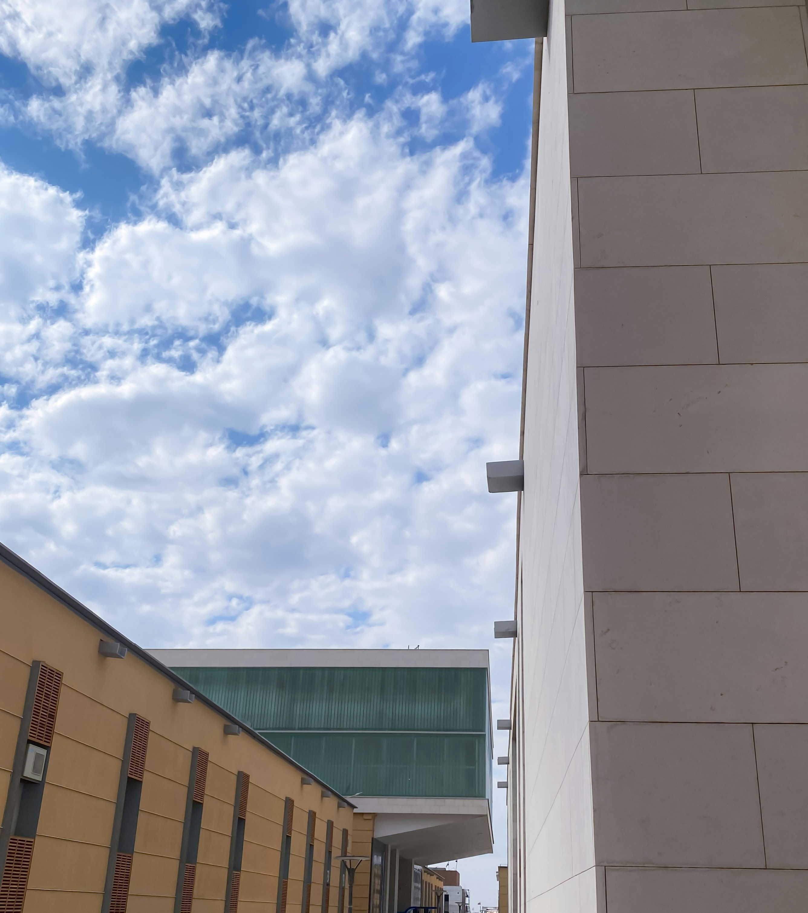 Modern architectural structures with a backdrop of scattered clouds in a blue sky.