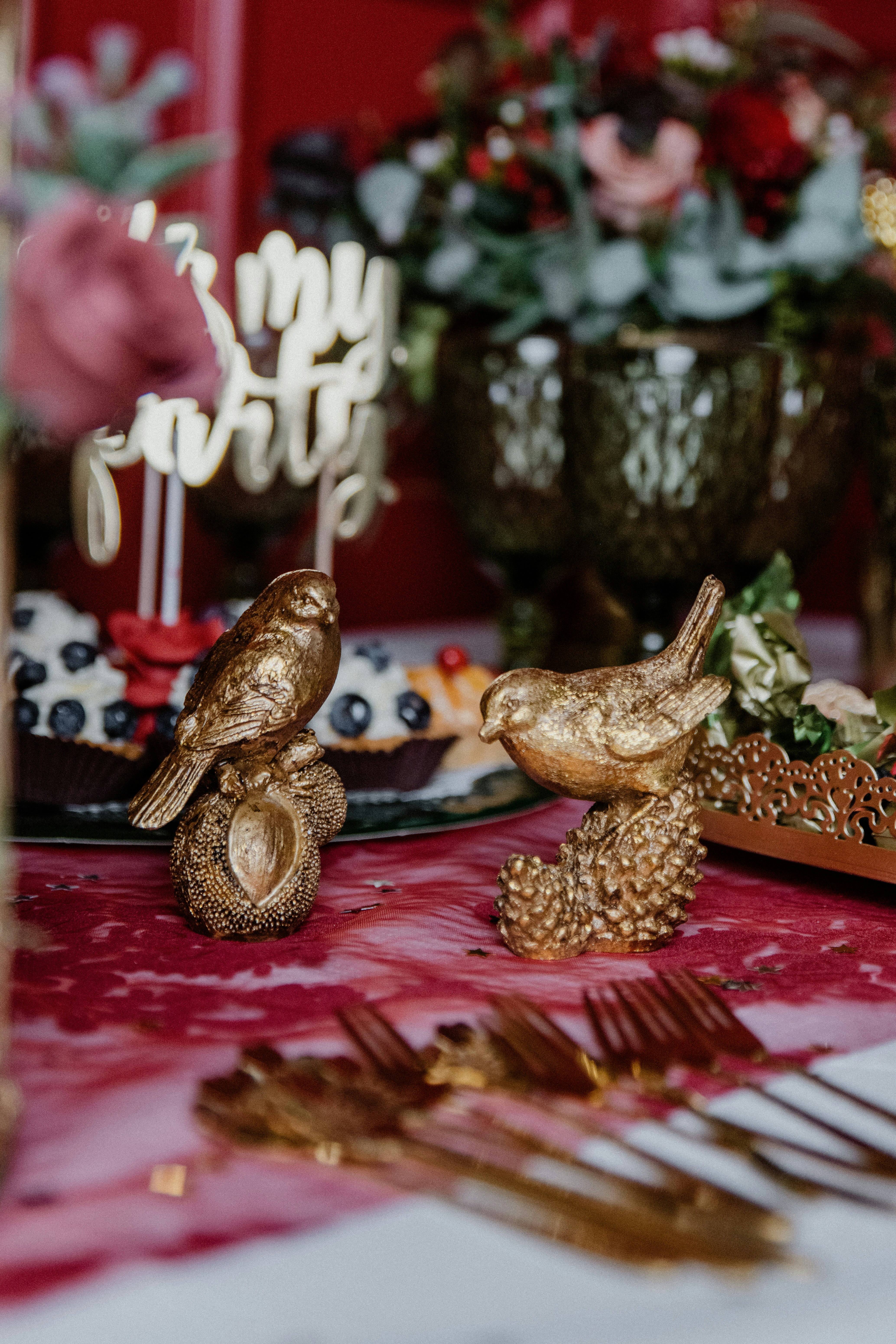 Two gilded songbirds guard a velvet-red dessert table