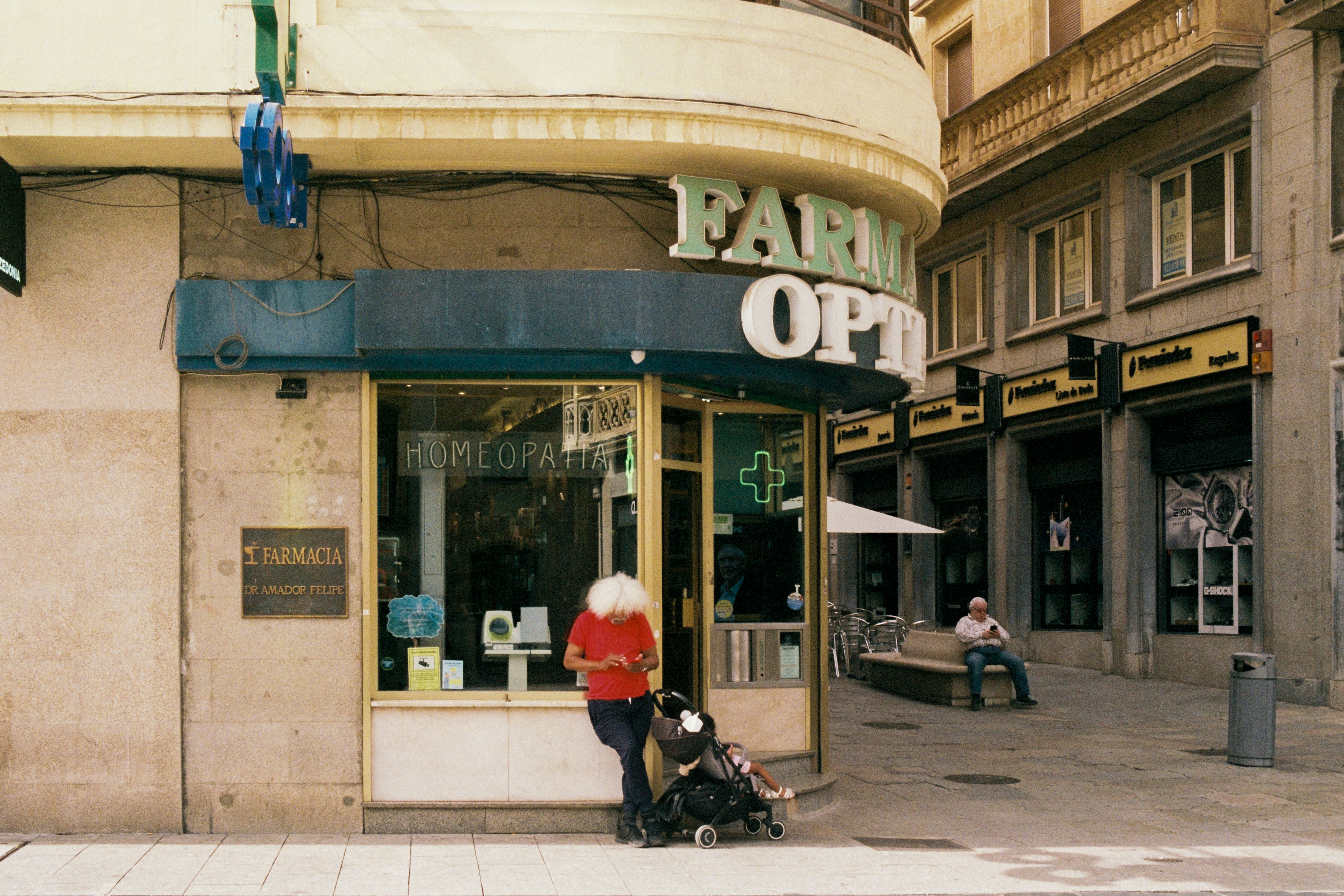 Person walking past a pharmacy with a green cross symbol on a city street.