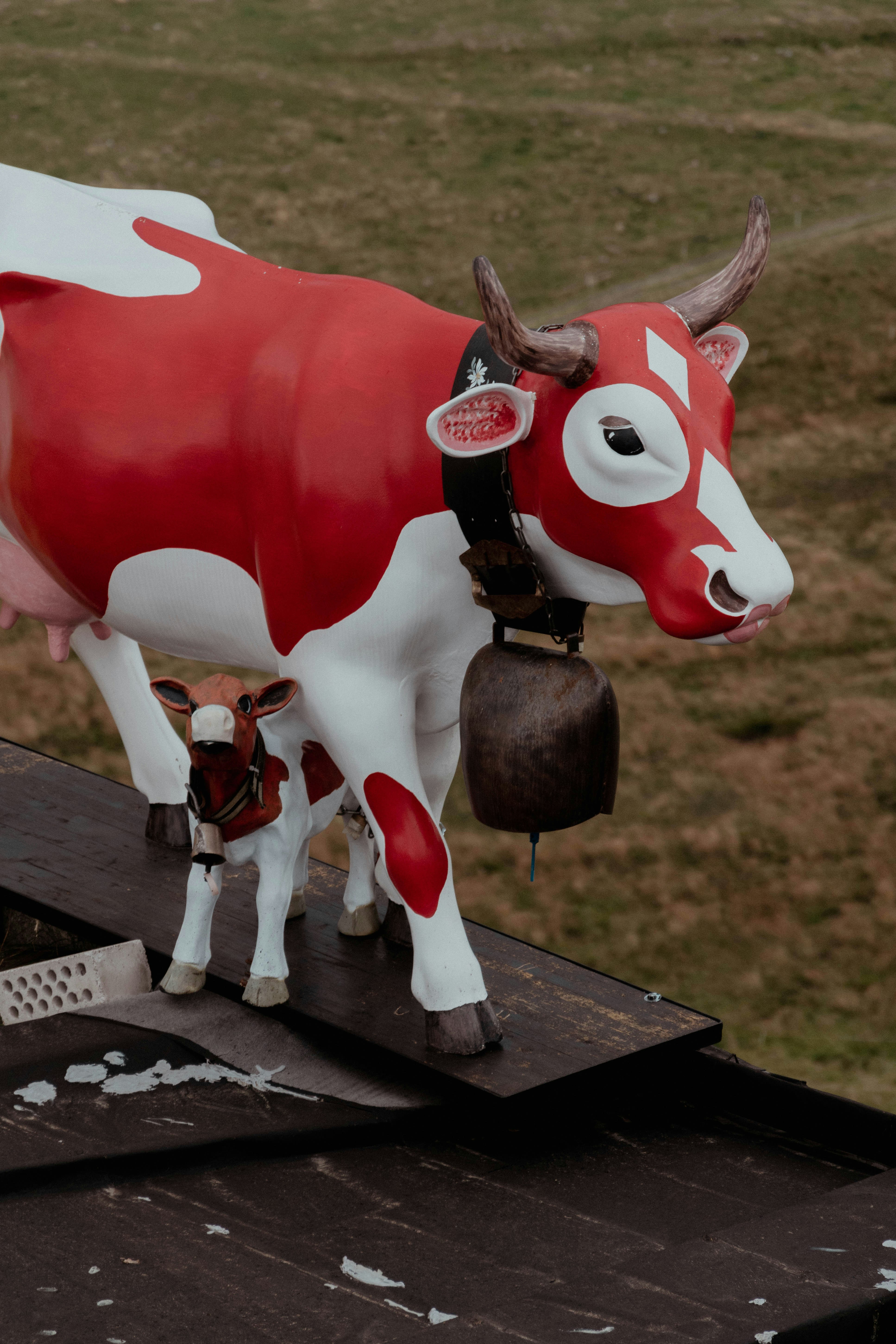 Red-Cow Sculpture: A Farmyard Bell and Painted Pair on a Weathered Roof