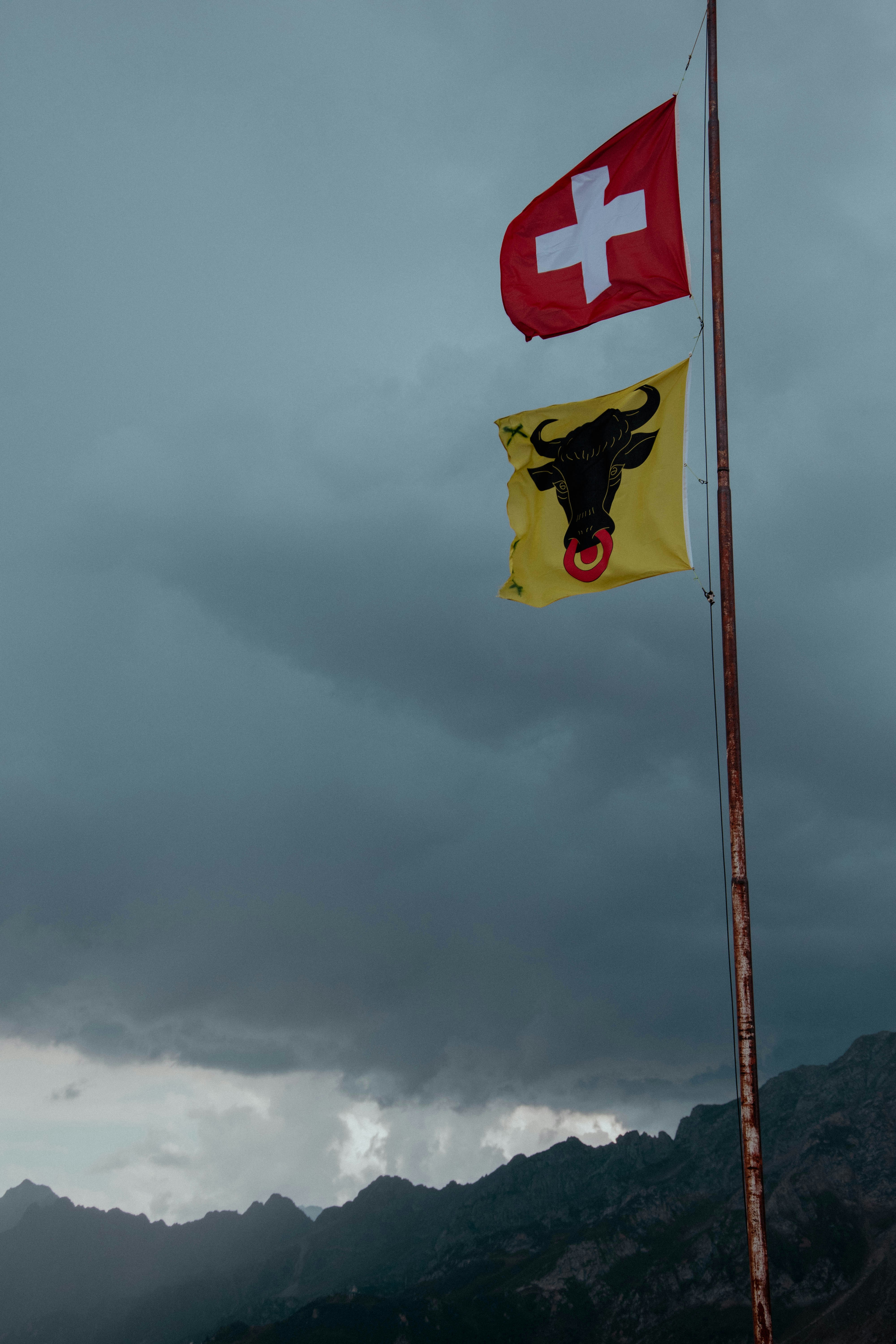 Twin Flags Against a Stormy Alpine Ridge: Swiss Cross Overcast Scene