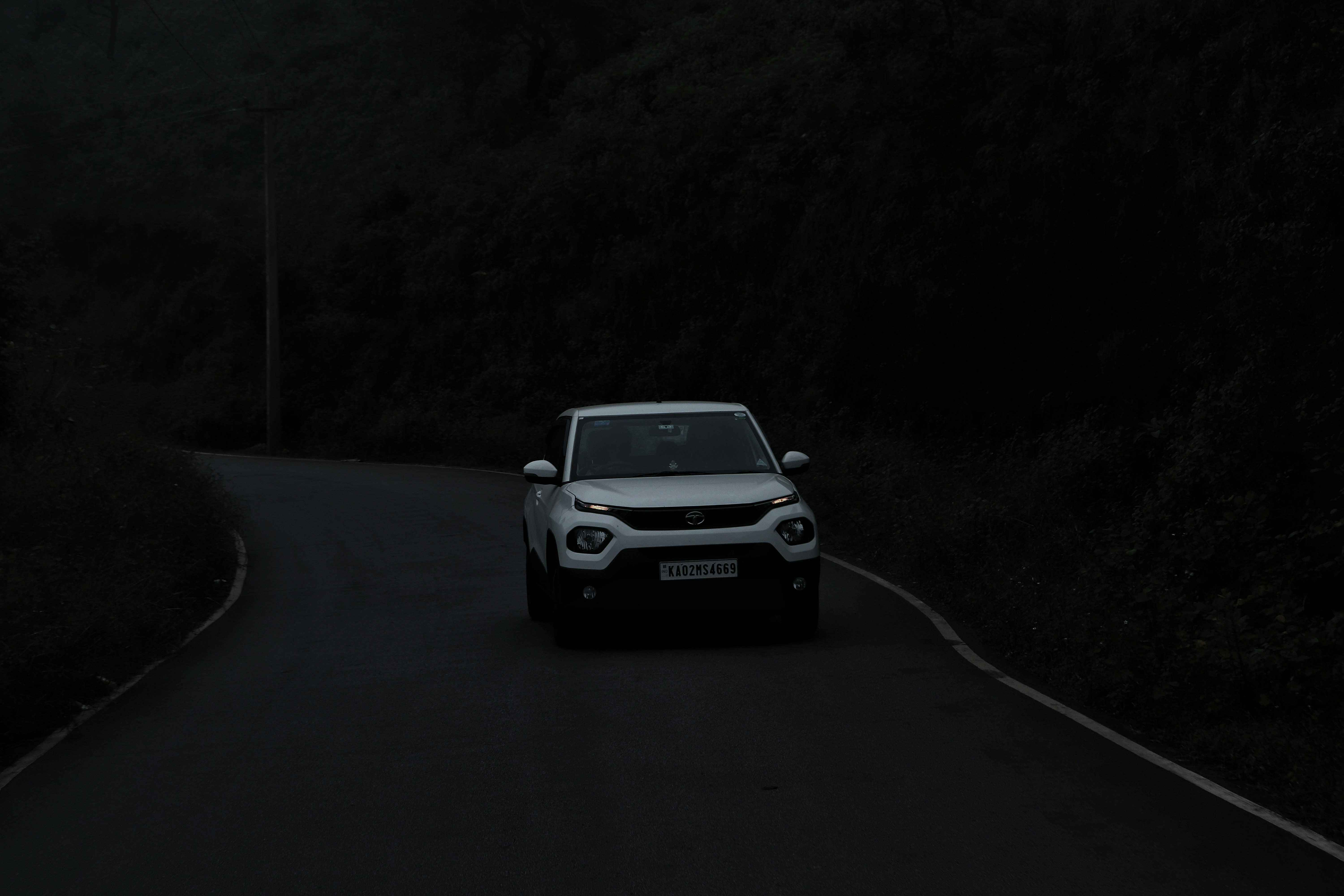 White SUV navigating a winding road surrounded by shadowy hills at dusk.
