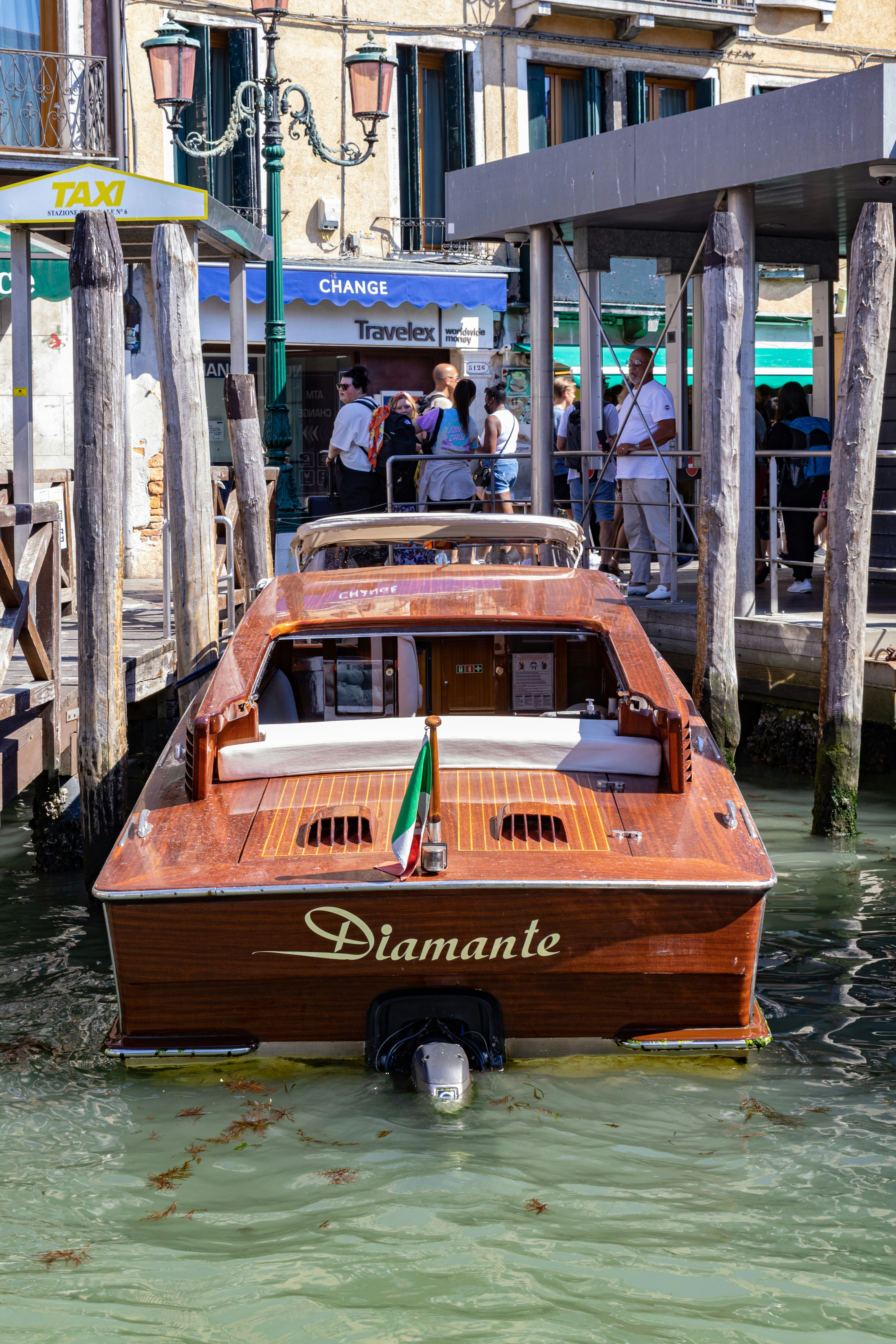 Diamante at Venice Canal: A Timeless Wooden Speedboat Docked Amid a Lively Venetian Pier
