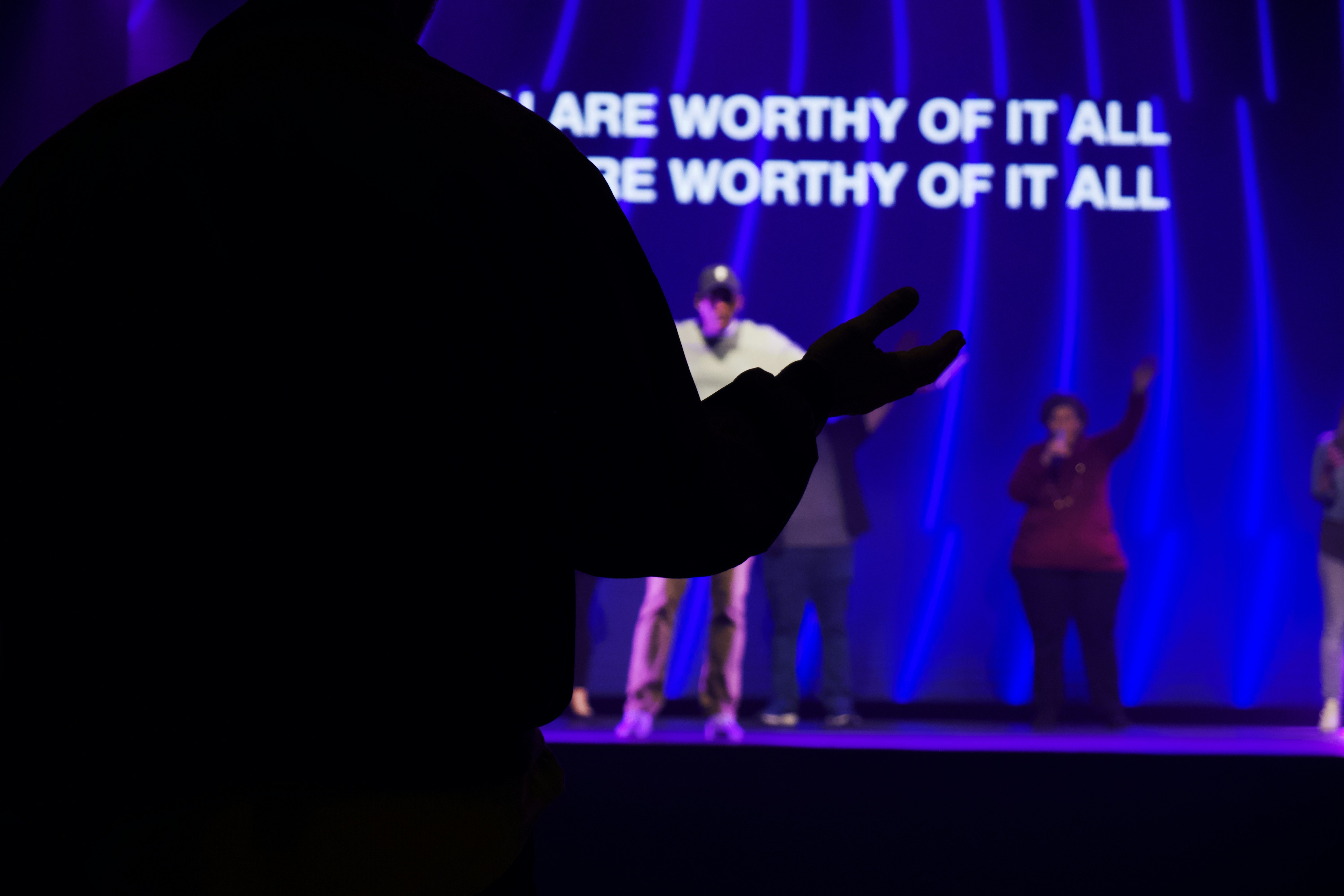 Silhouetted Listener Faces a Stage of Voices