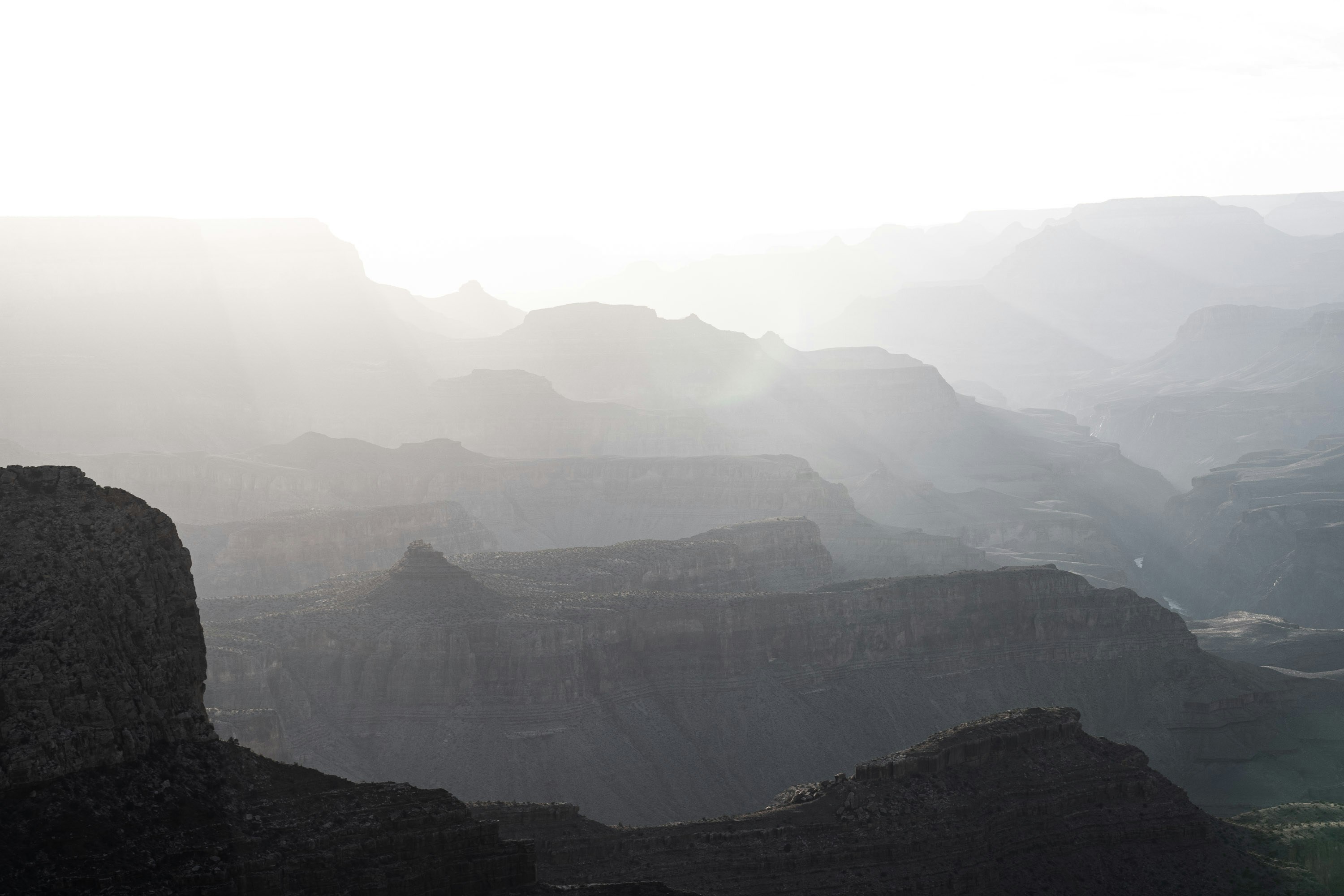 Soft rays of sunlight filter through the canyon, revealing layered rock formations and a sense of depth in the landscape.